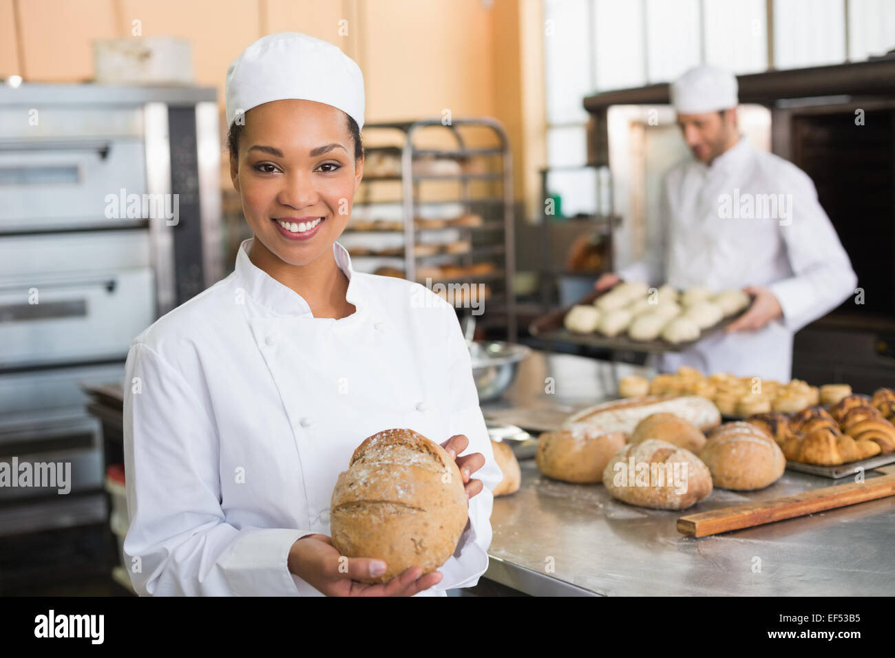 Pretty baker smiling at camera with loaf Stock Photo - Alamy