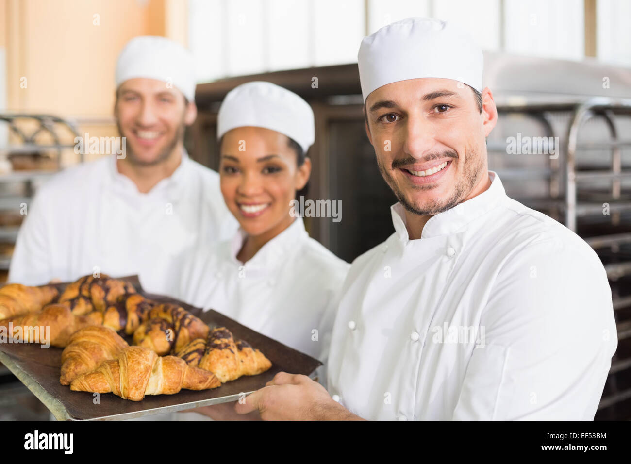 Team of bakers smiling at camera with trays of croissants Stock Photo ...