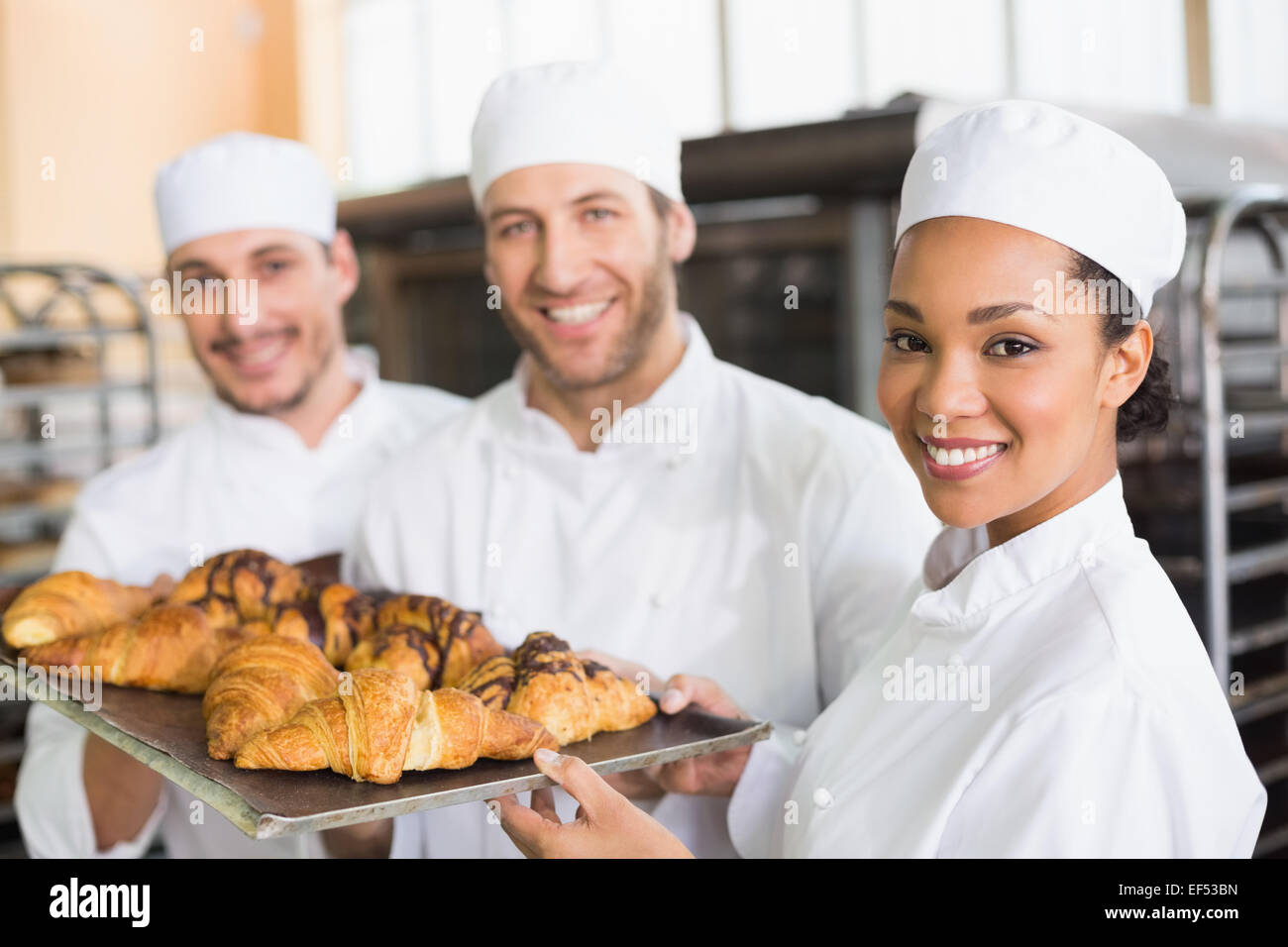 Team of bakers smiling at camera with trays of croissants Stock Photo ...