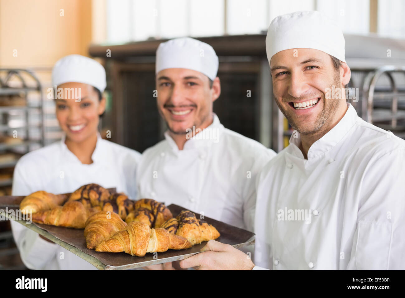 Team of bakers smiling at camera with trays of croissants Stock Photo ...