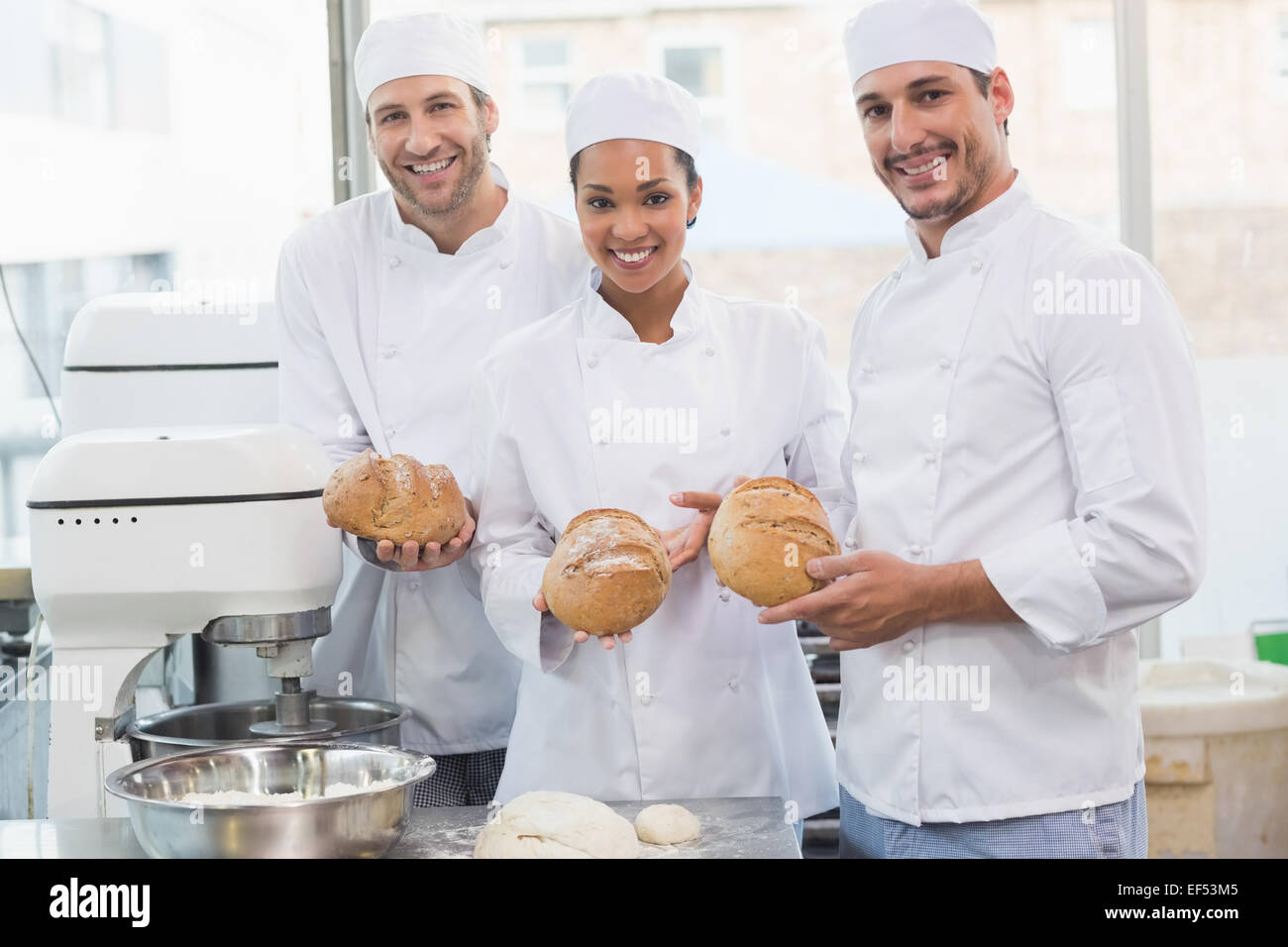 Team of bakers smiling at camera holding bread Stock Photo - Alamy