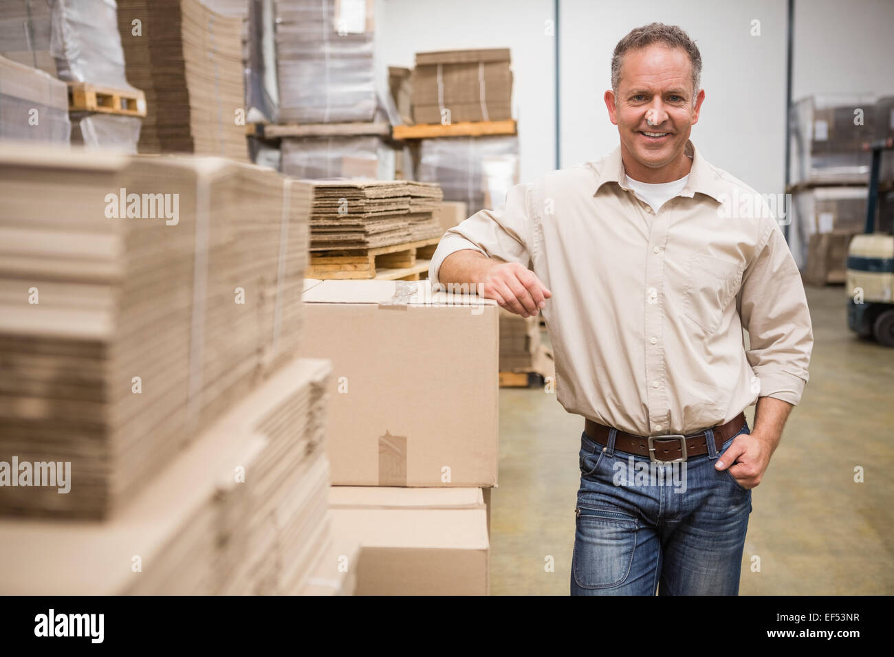 Smiling warehouse worker leaning against boxes Stock Photo - Alamy