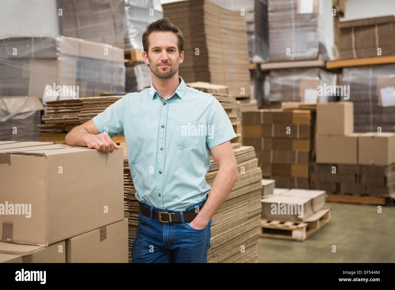 Smiling warehouse worker leaning against boxes Stock Photo - Alamy