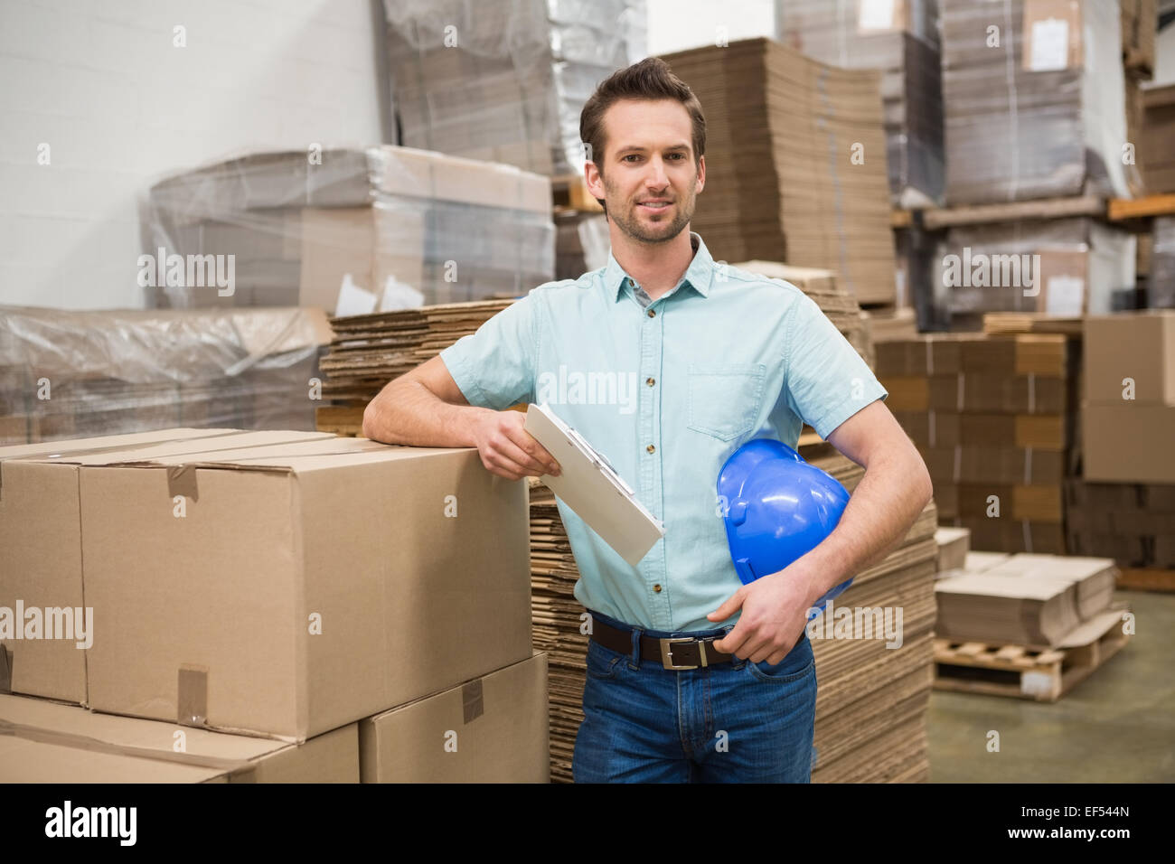 Smiling warehouse worker leaning against boxes Stock Photo - Alamy