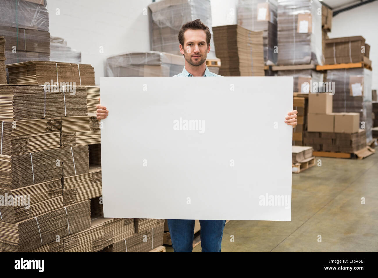 Smiling warehouse worker holding large white poster Stock Photo - Alamy