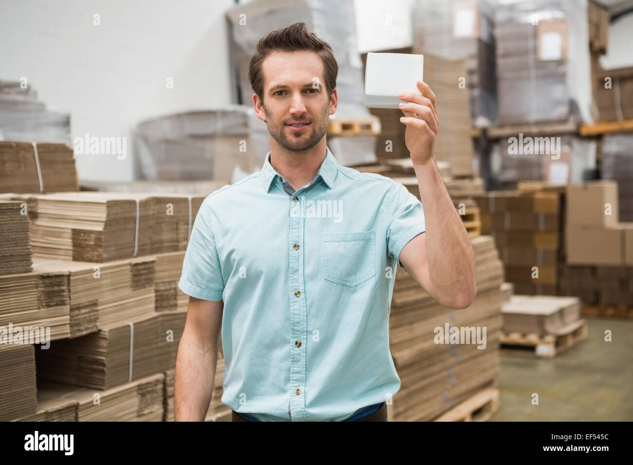 Smiling warehouse worker showing a small box Stock Photo - Alamy