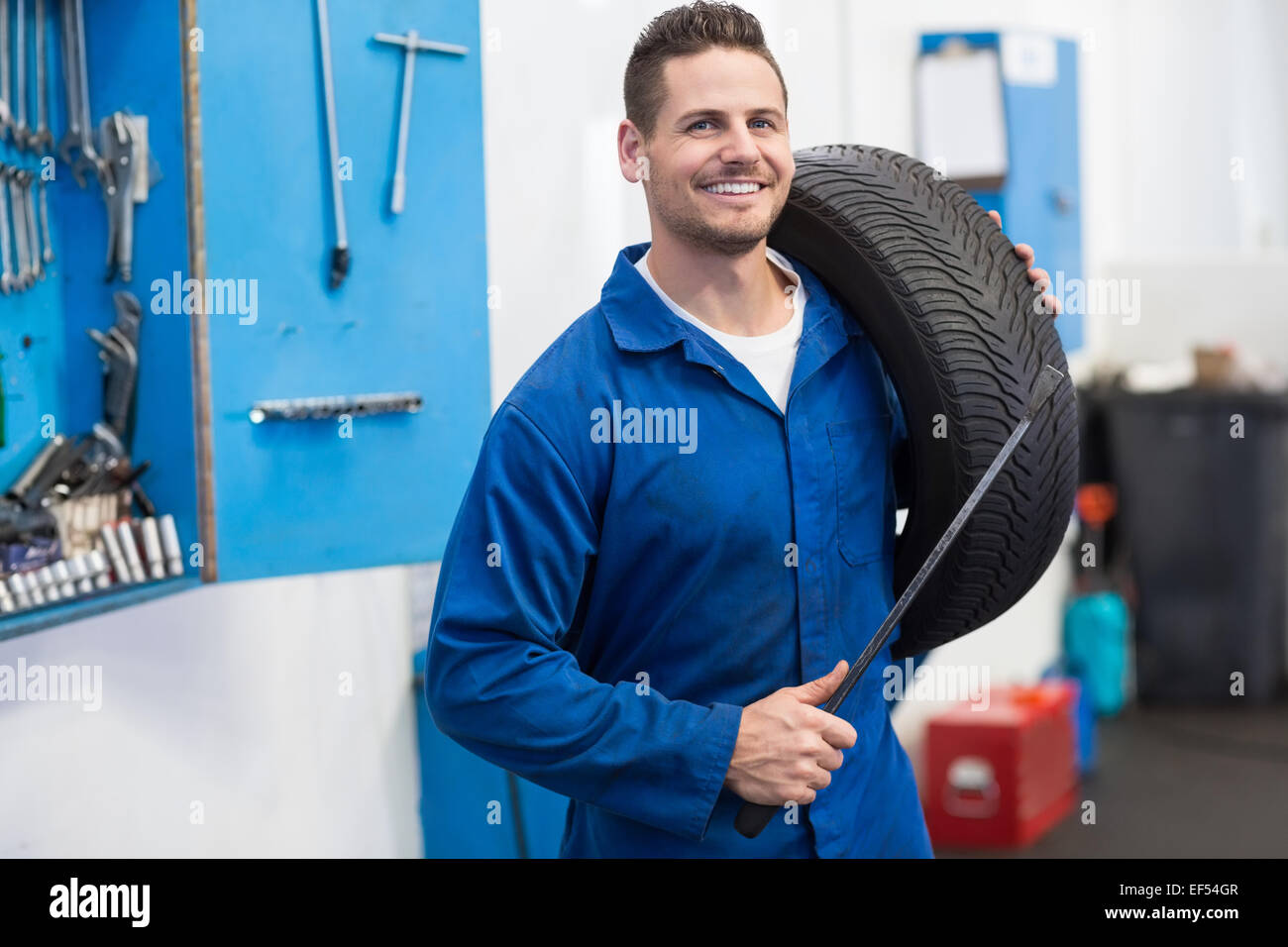 Mechanic smiling at the camera holding tire Stock Photo - Alamy