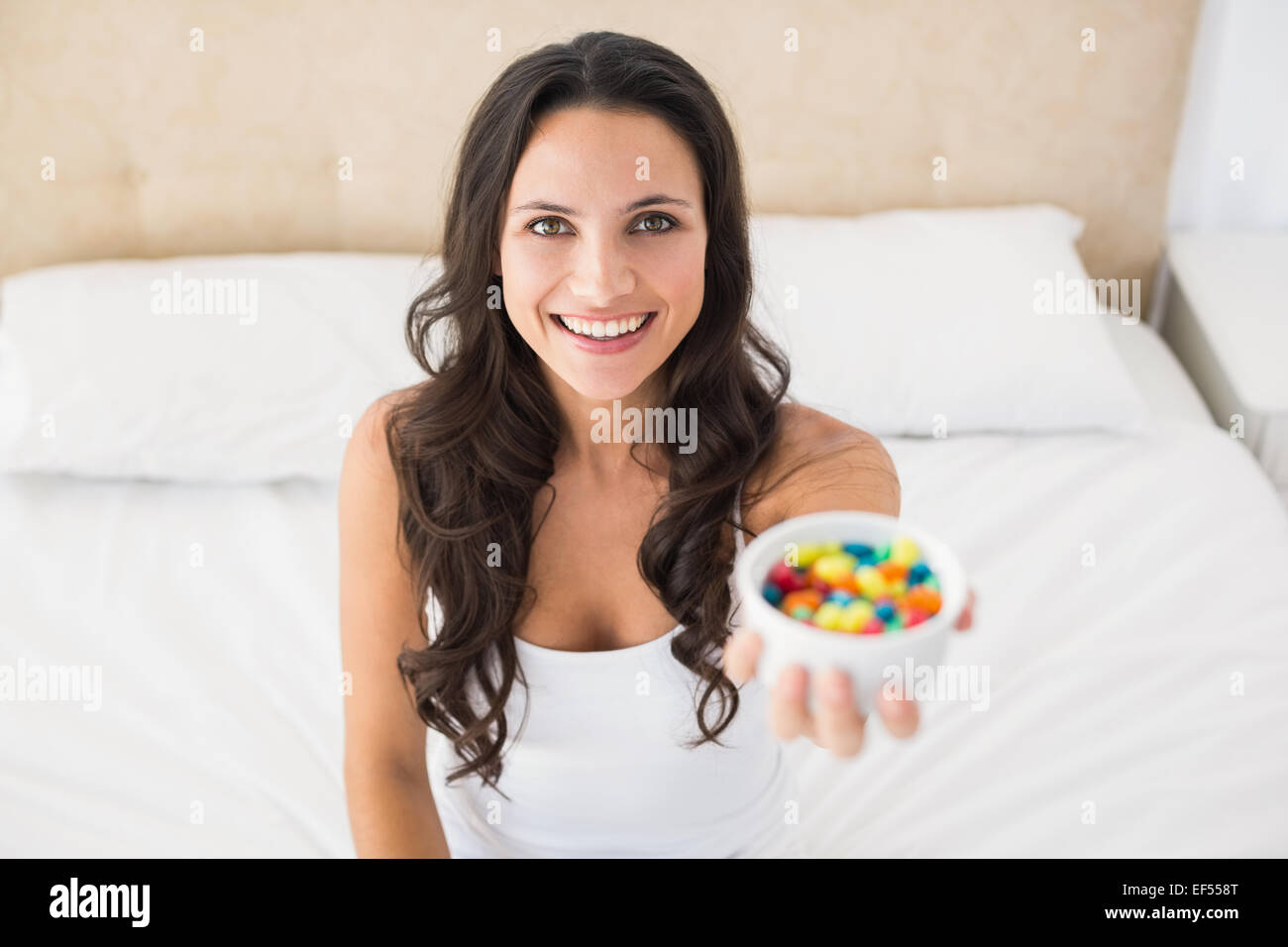 Pretty brunette offering candy in bed Stock Photo - Alamy