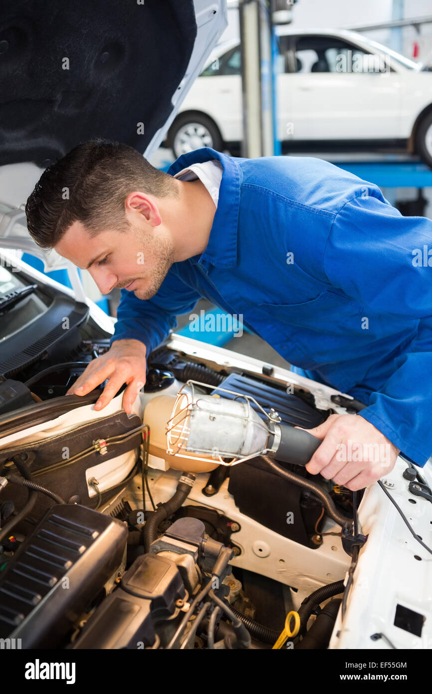 Mechanic examining under hood of car with torch Stock Photo - Alamy