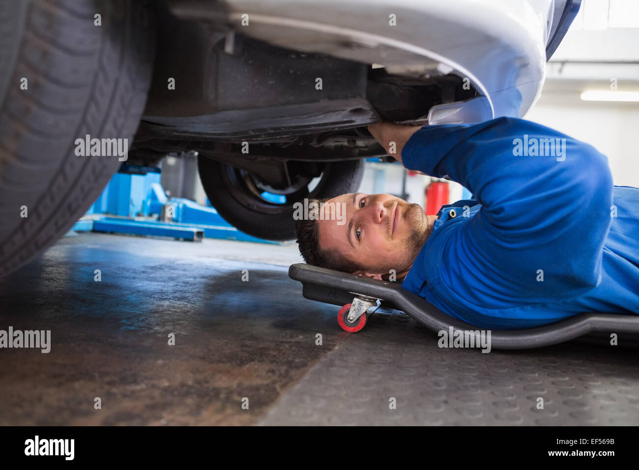 Smiling mechanic lying on trolley Stock Photo - Alamy