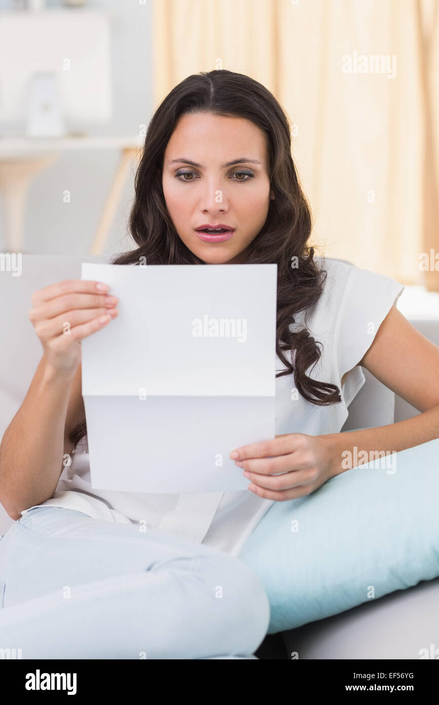 Shocked brunette reading letter on couch Stock Photo - Alamy