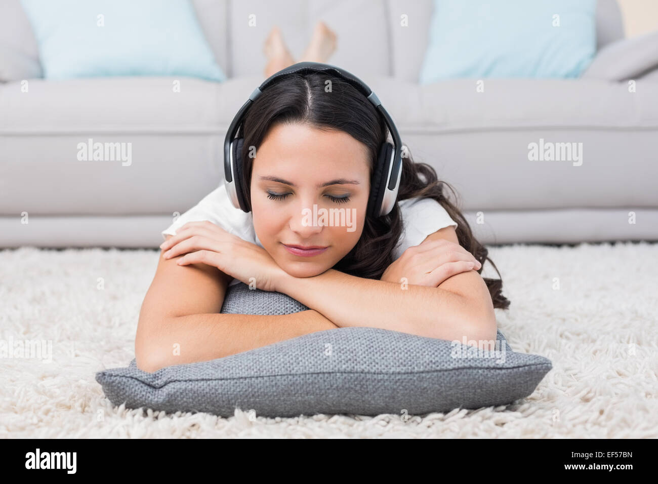 Pretty brunette lying on the rug listening to music Stock Photo - Alamy
