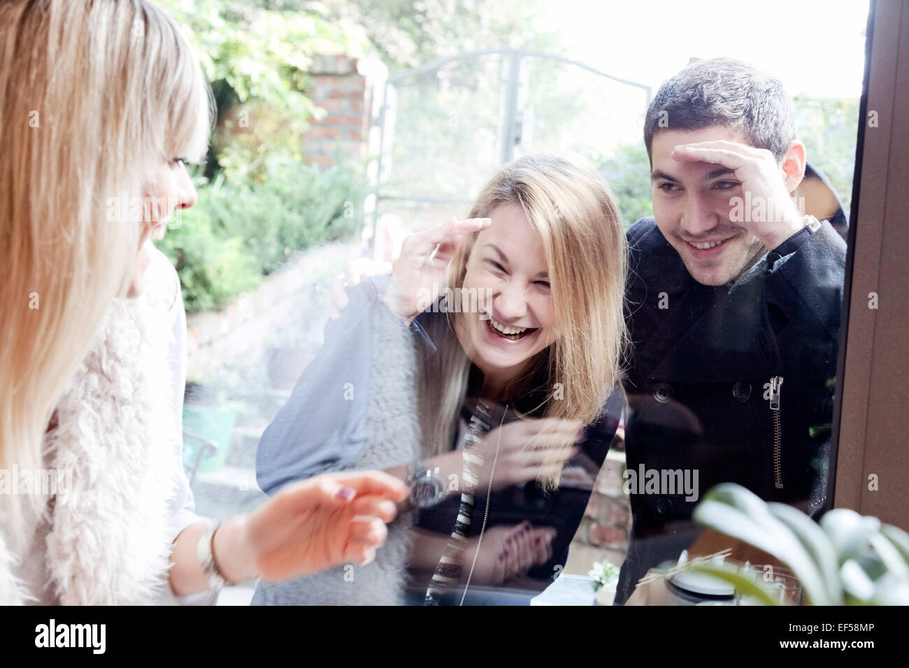 Friends looking through window Stock Photo - Alamy