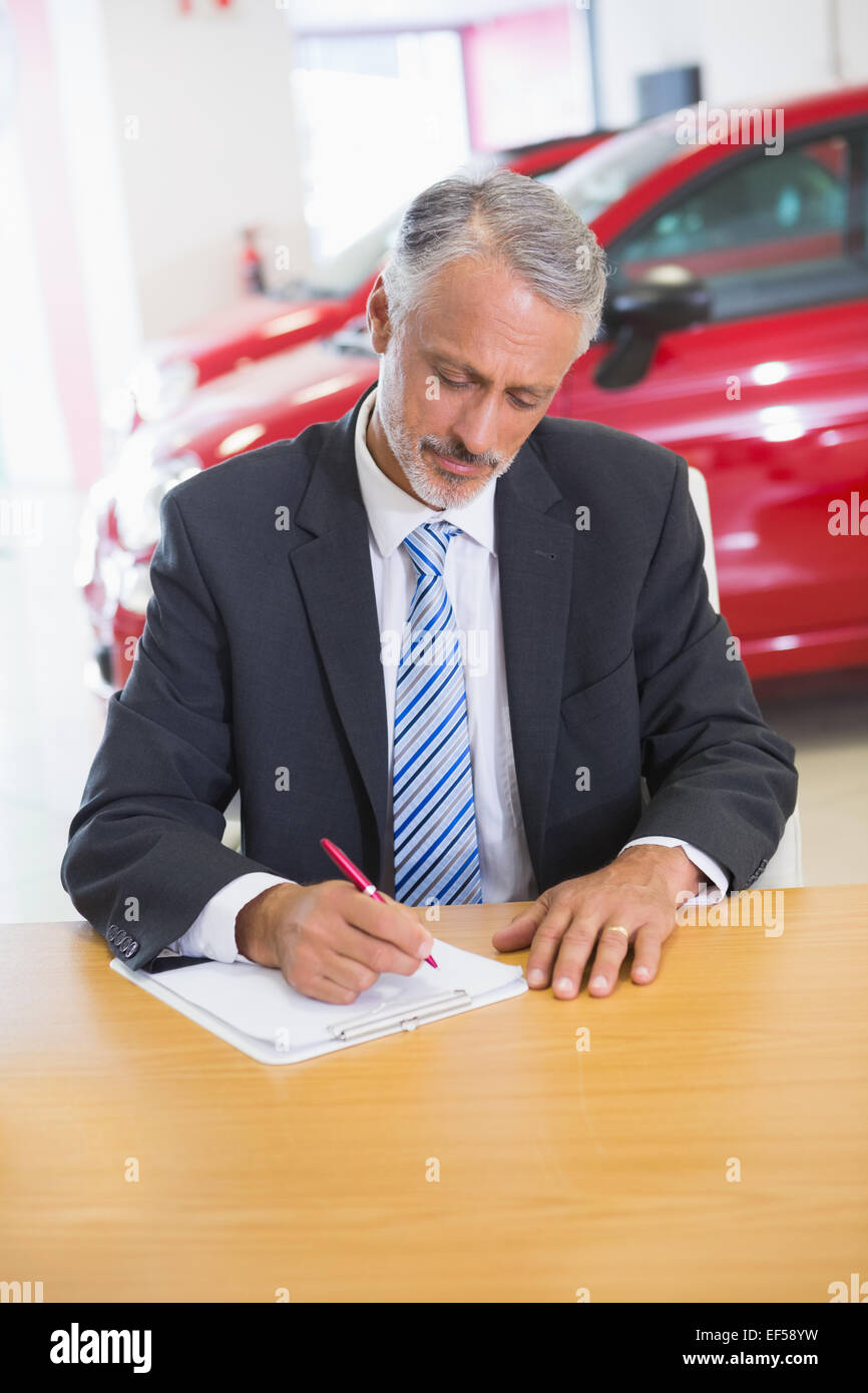 Focused salesman writing on clipboard at his desk Stock Photo - Alamy