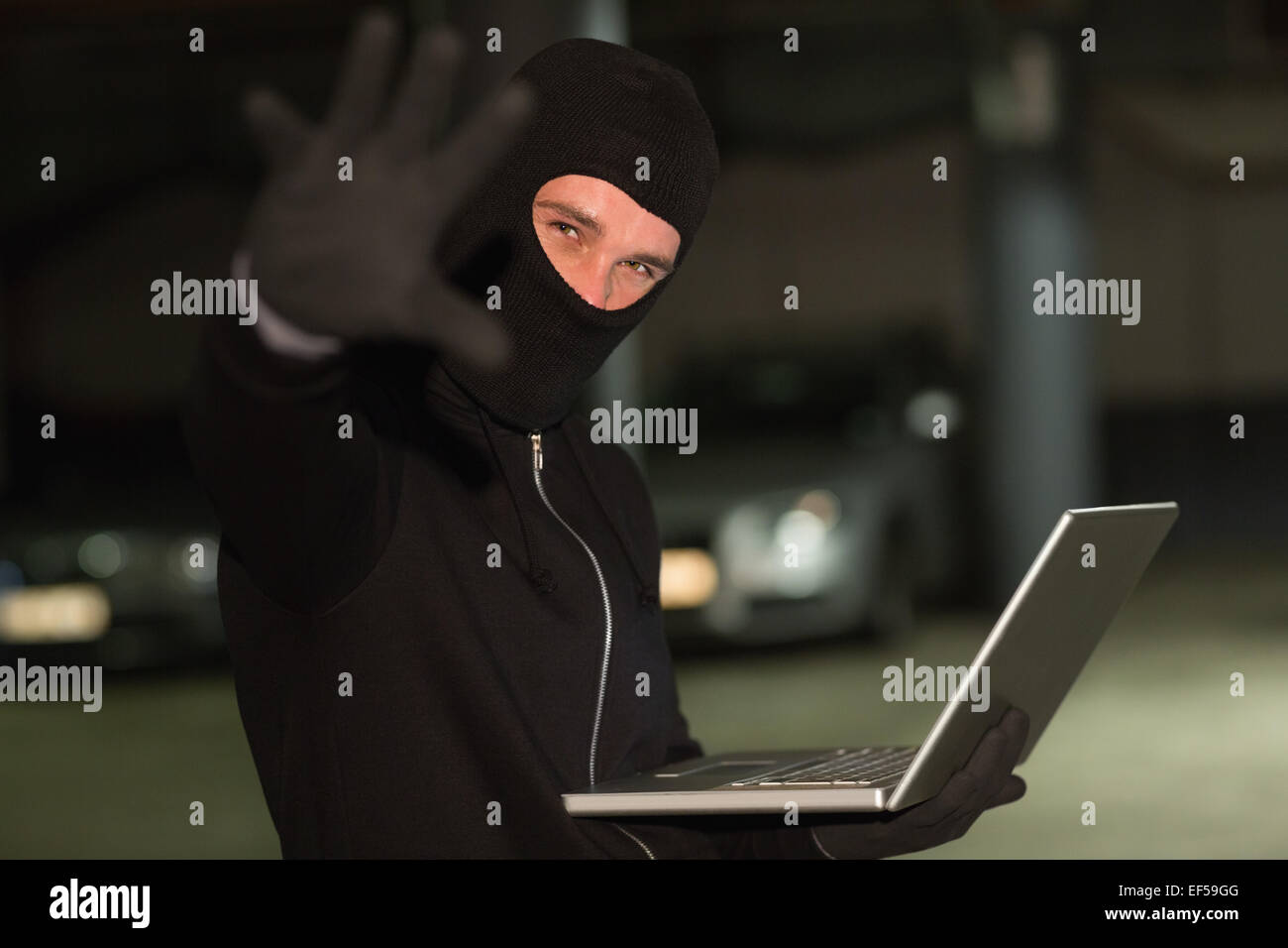 Hacker in balaclava gesturing and using laptop Stock Photo - Alamy