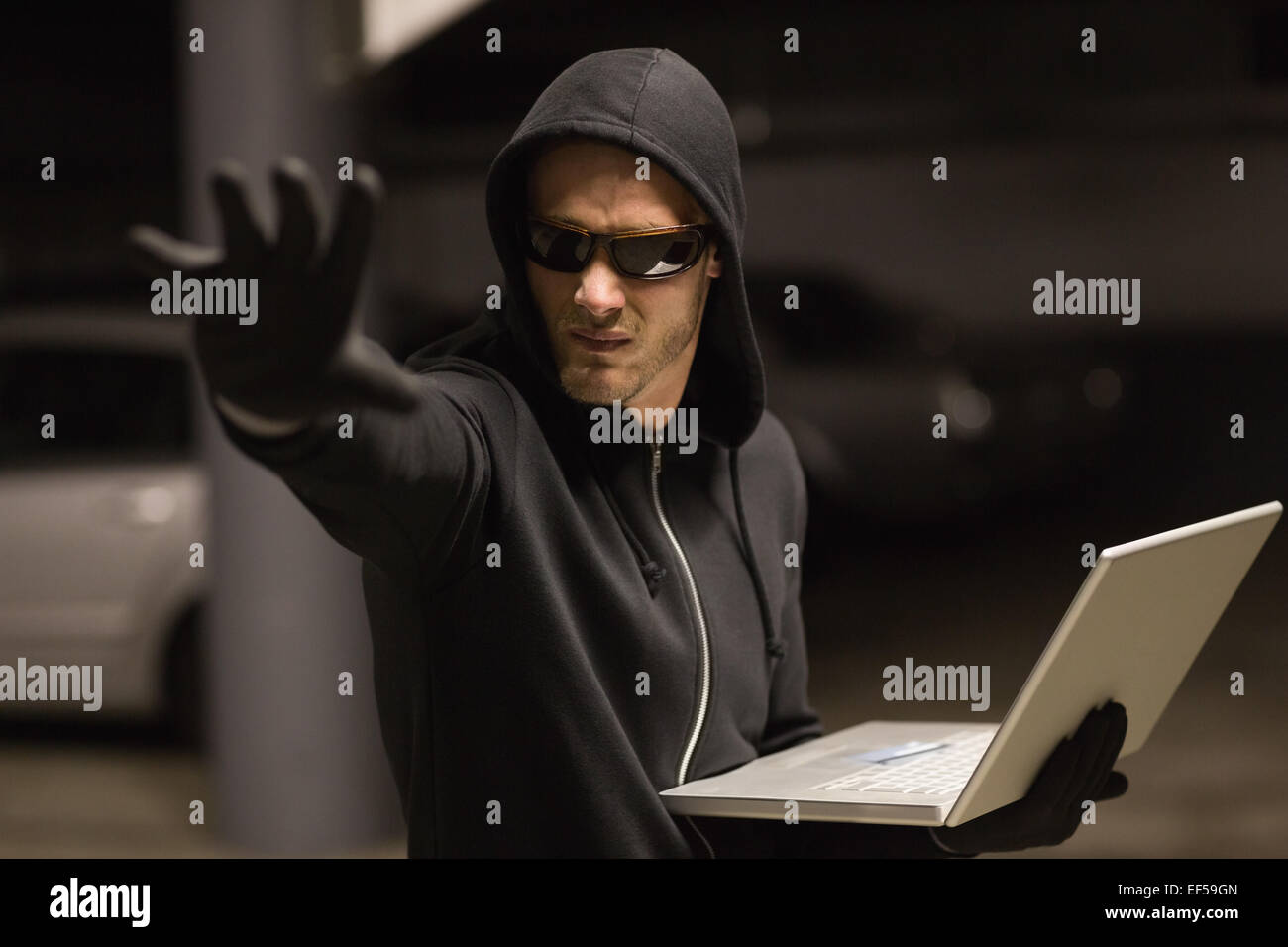 Hacker in balaclava gesturing and using laptop Stock Photo - Alamy
