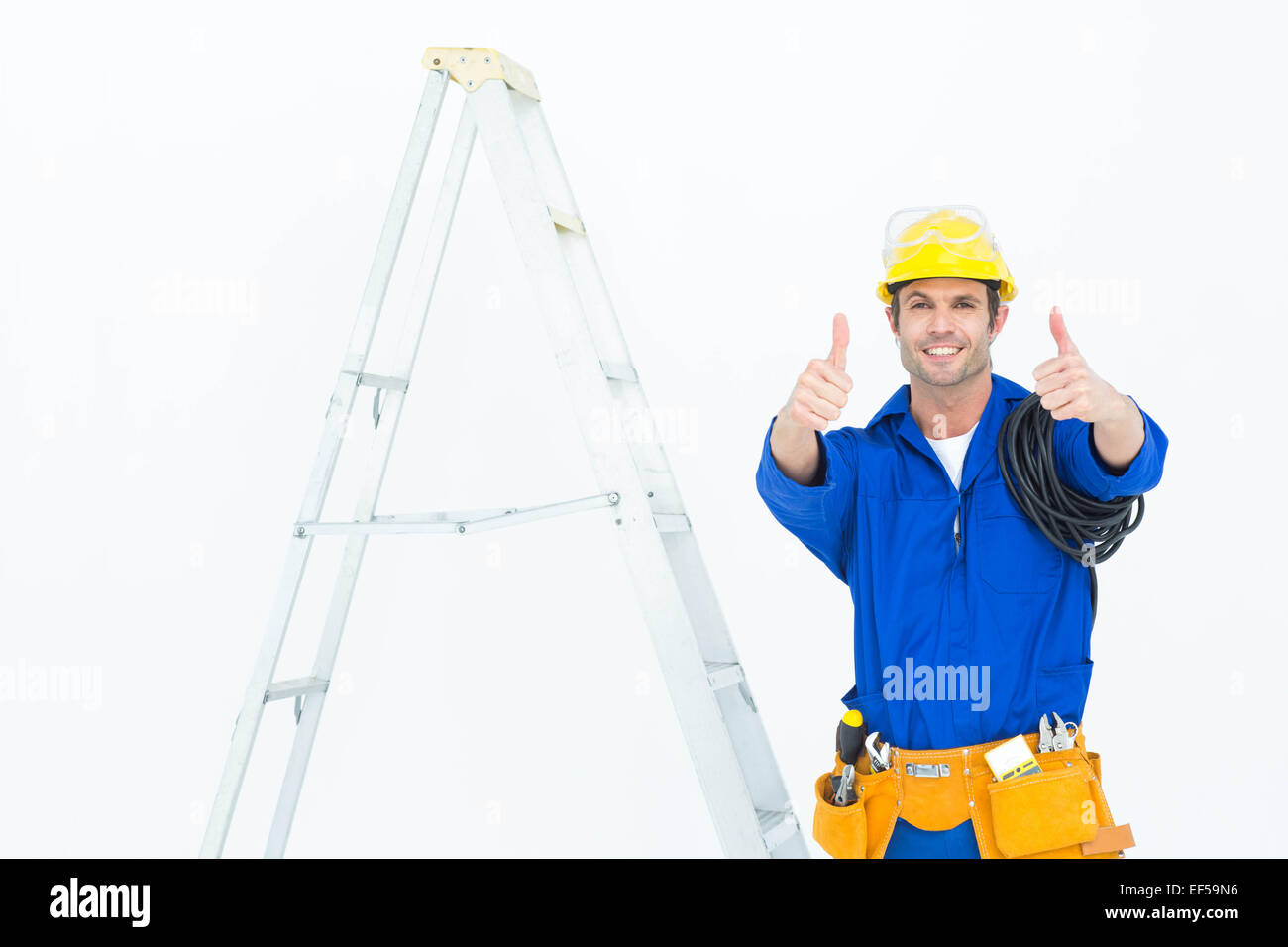 Happy electrician gesturing thumbs up by ladder Stock Photo - Alamy