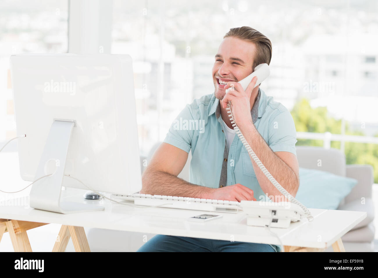Smiling businessman on the phone while using computer Stock Photo - Alamy