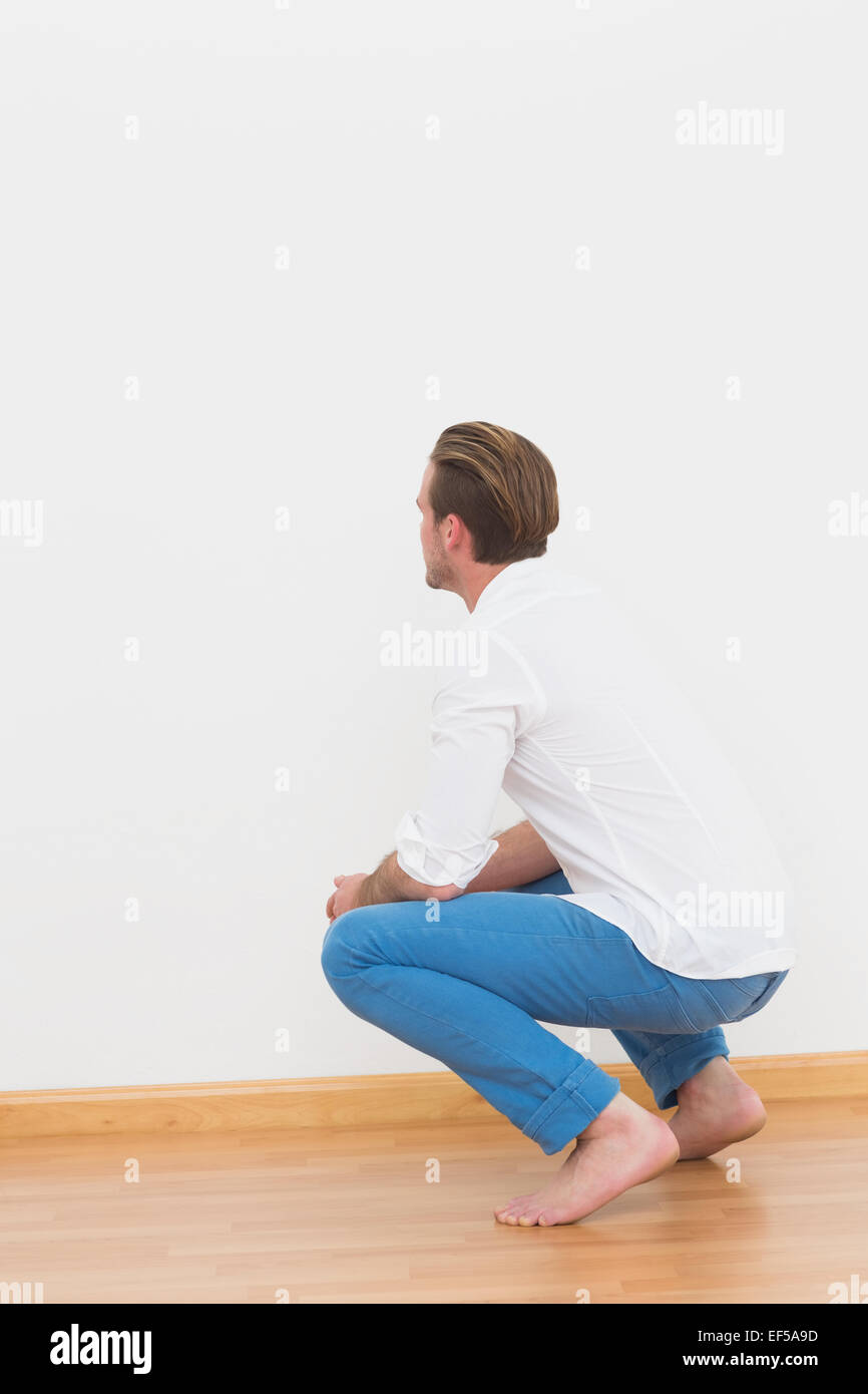 Casual man crouching on floor looking at wall Stock Photo - Alamy