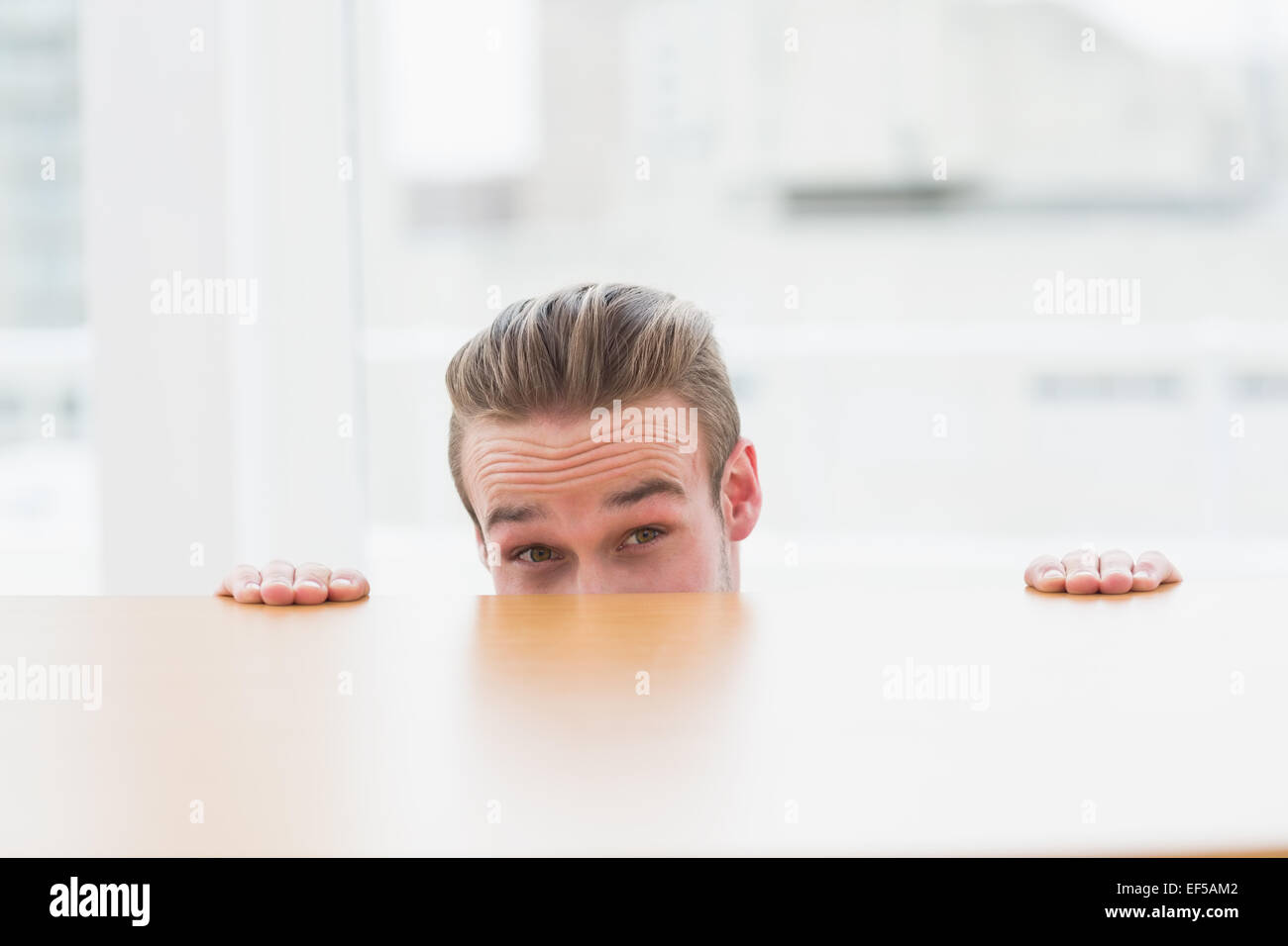 Nervous businessman peeking over desk Stock Photo - Alamy
