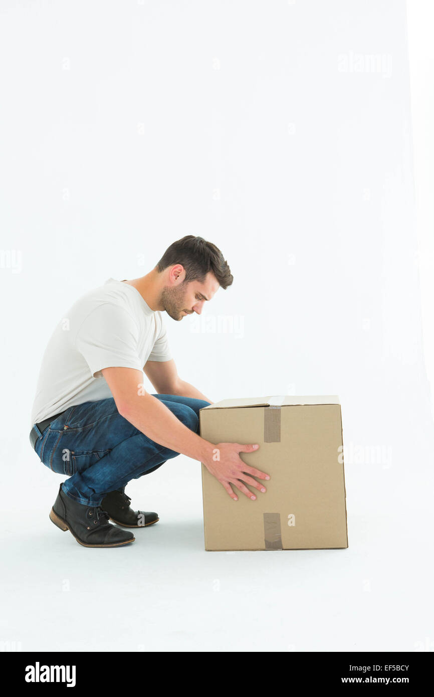 Delivery man crouching while picking cardboard box Stock Photo - Alamy