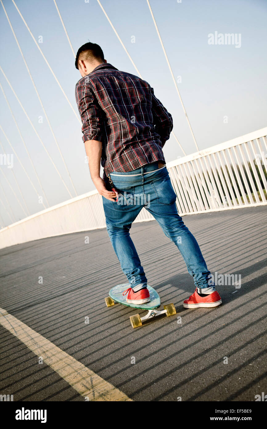 Young man skateboarding across bridge Stock Photo - Alamy