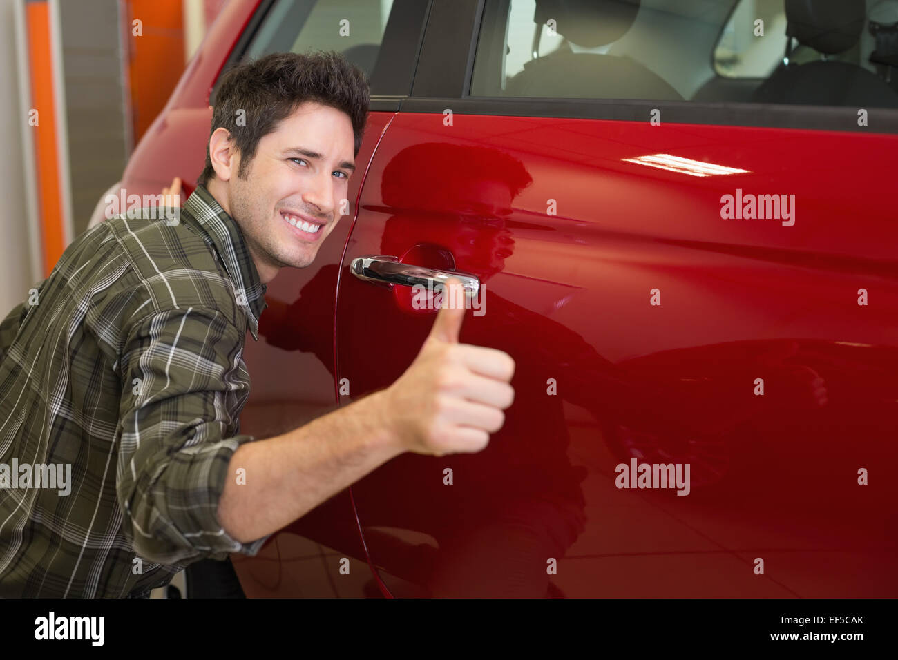 Smiling man hugging a red car while giving thumbs up Stock Photo - Alamy