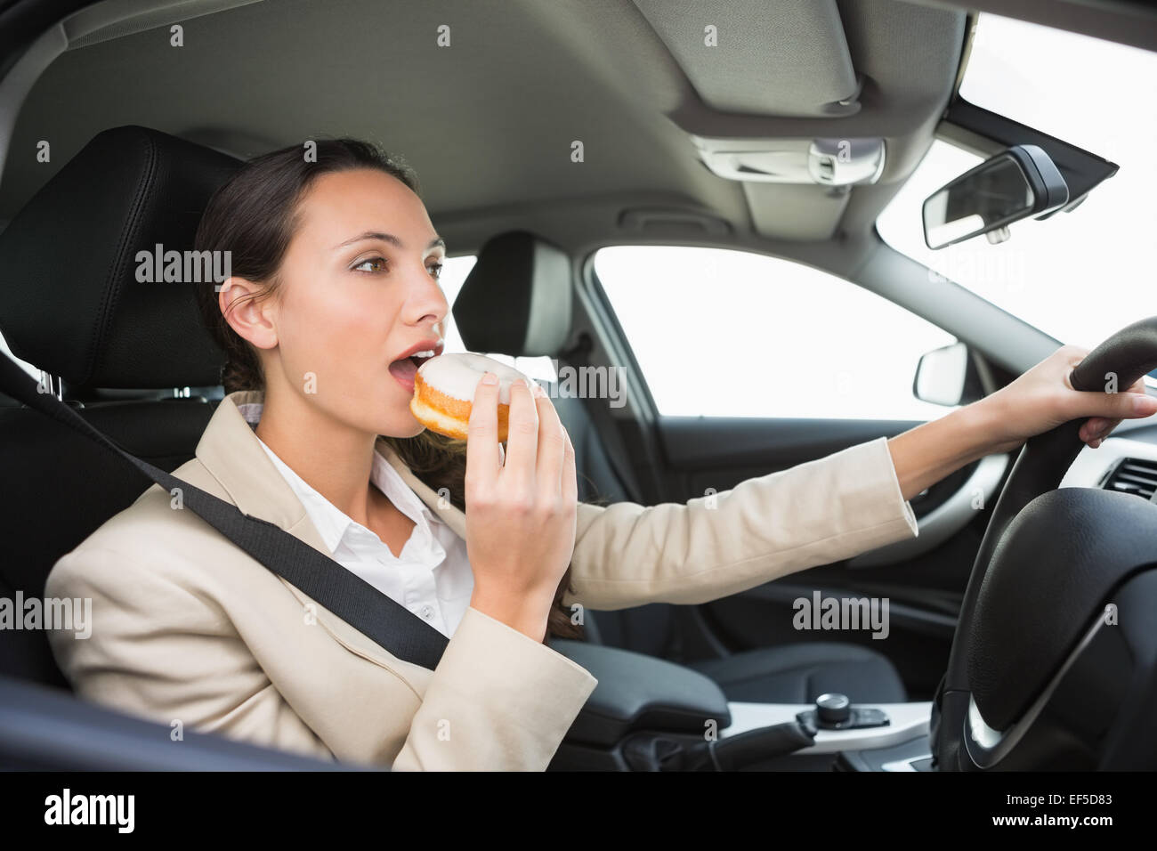 Pretty businesswoman having doughnut while driving Stock Photo - Alamy
