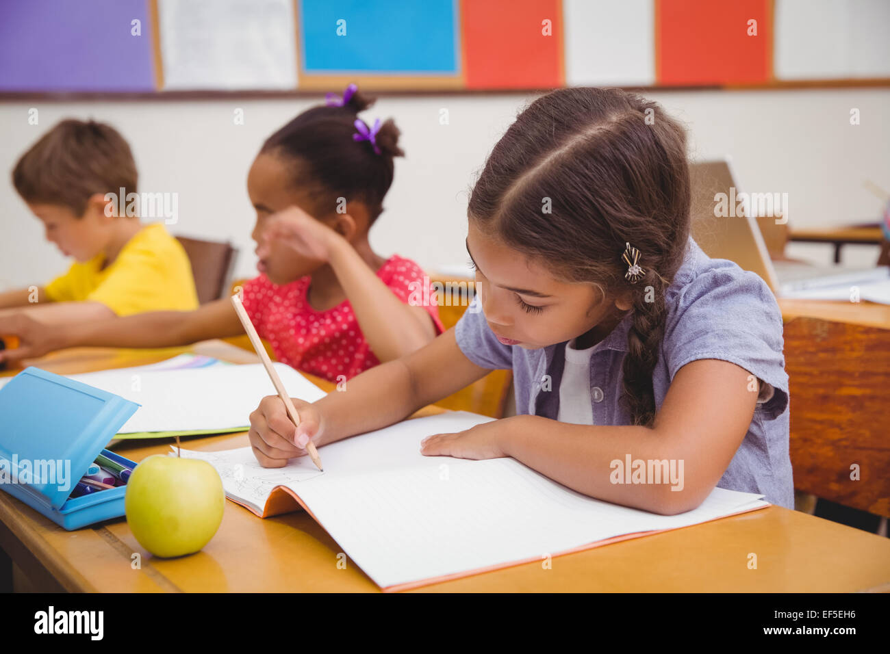 Cute pupils writing at desk in classroom Stock Photo - Alamy