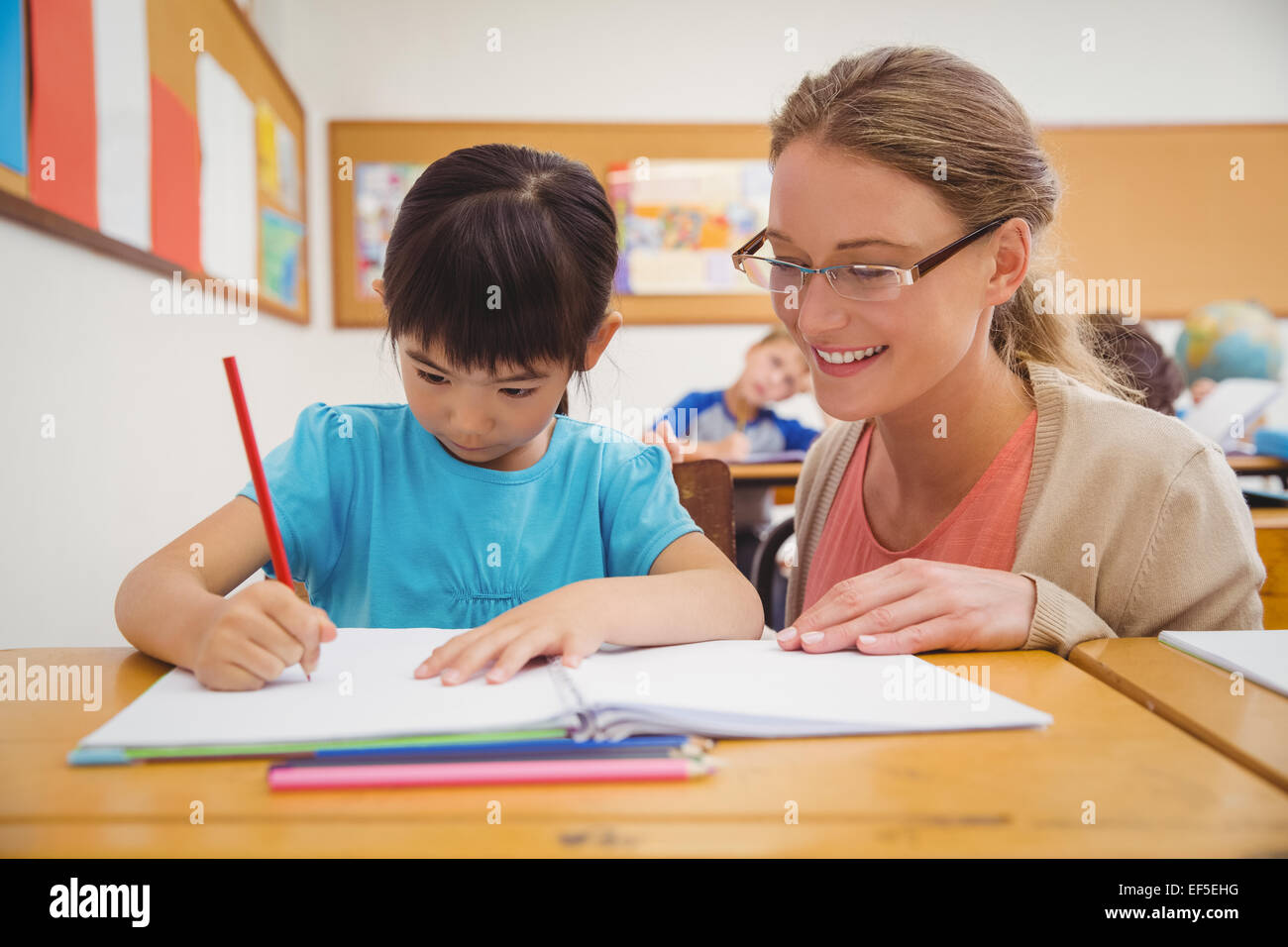 Pretty teacher helping pupil in classroom Stock Photo - Alamy