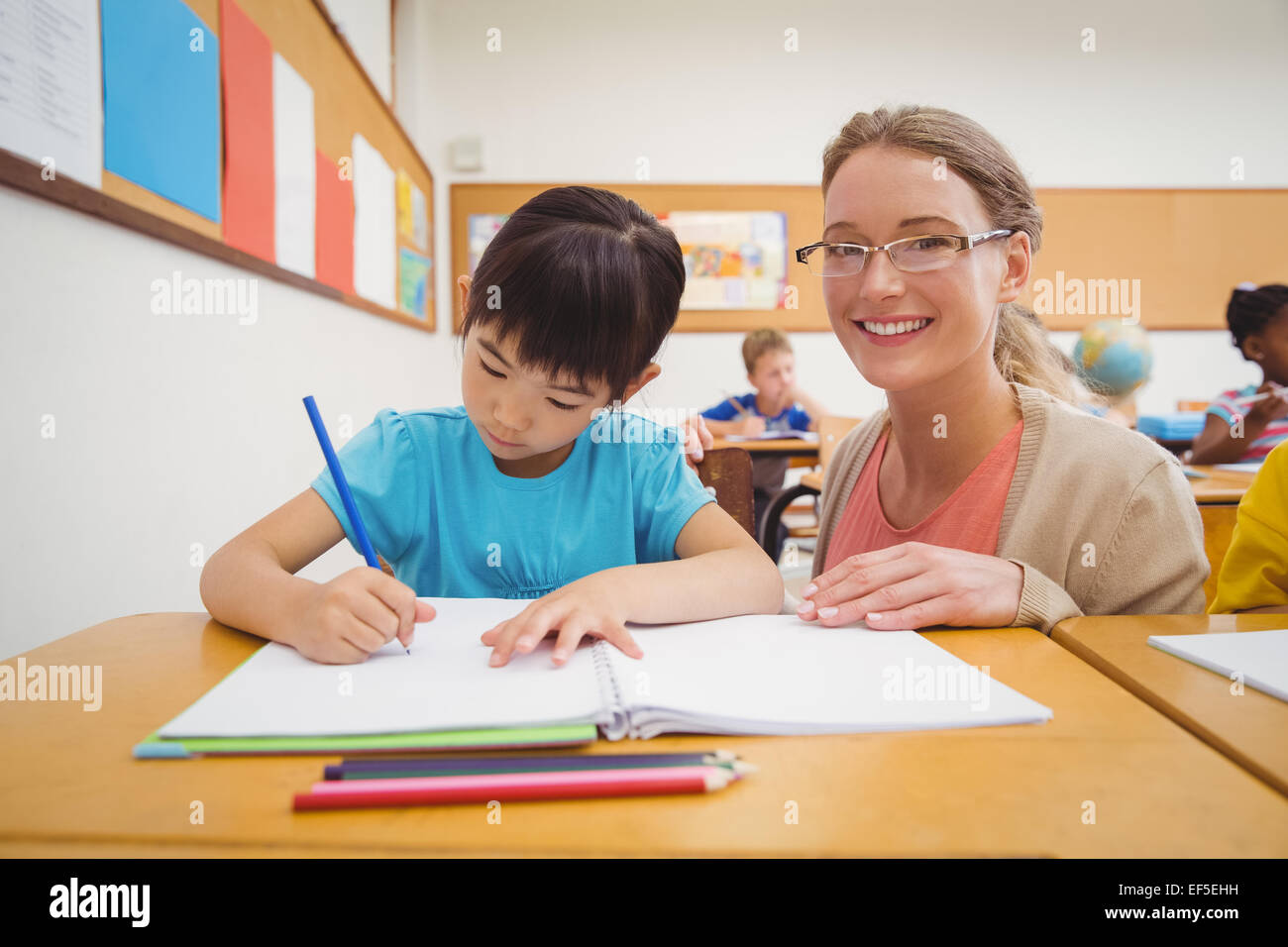 Pretty teacher helping pupil in classroom Stock Photo - Alamy