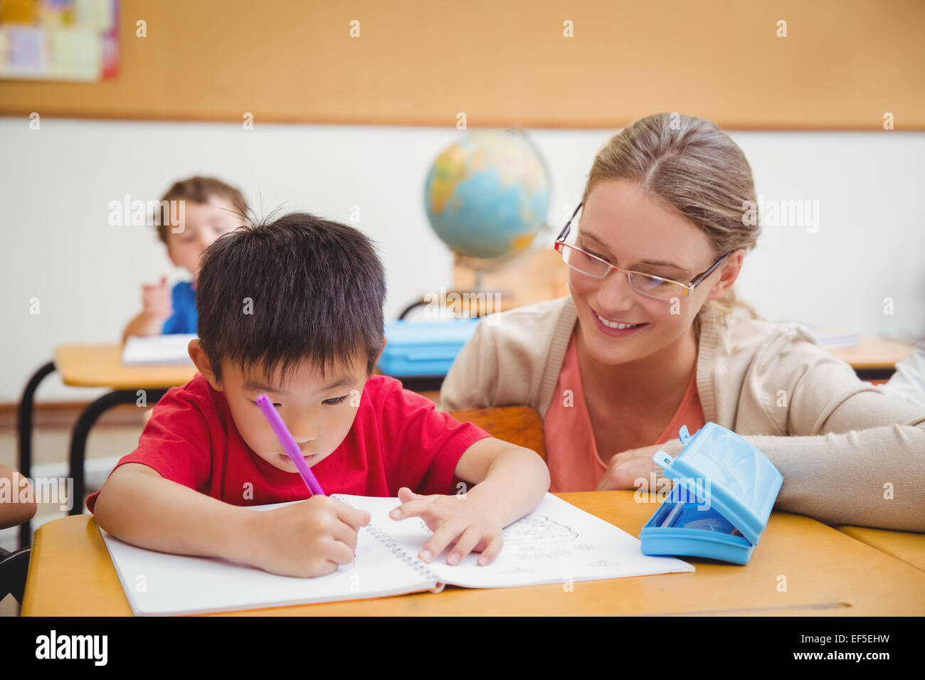 Pretty teacher helping pupil in classroom Stock Photo - Alamy