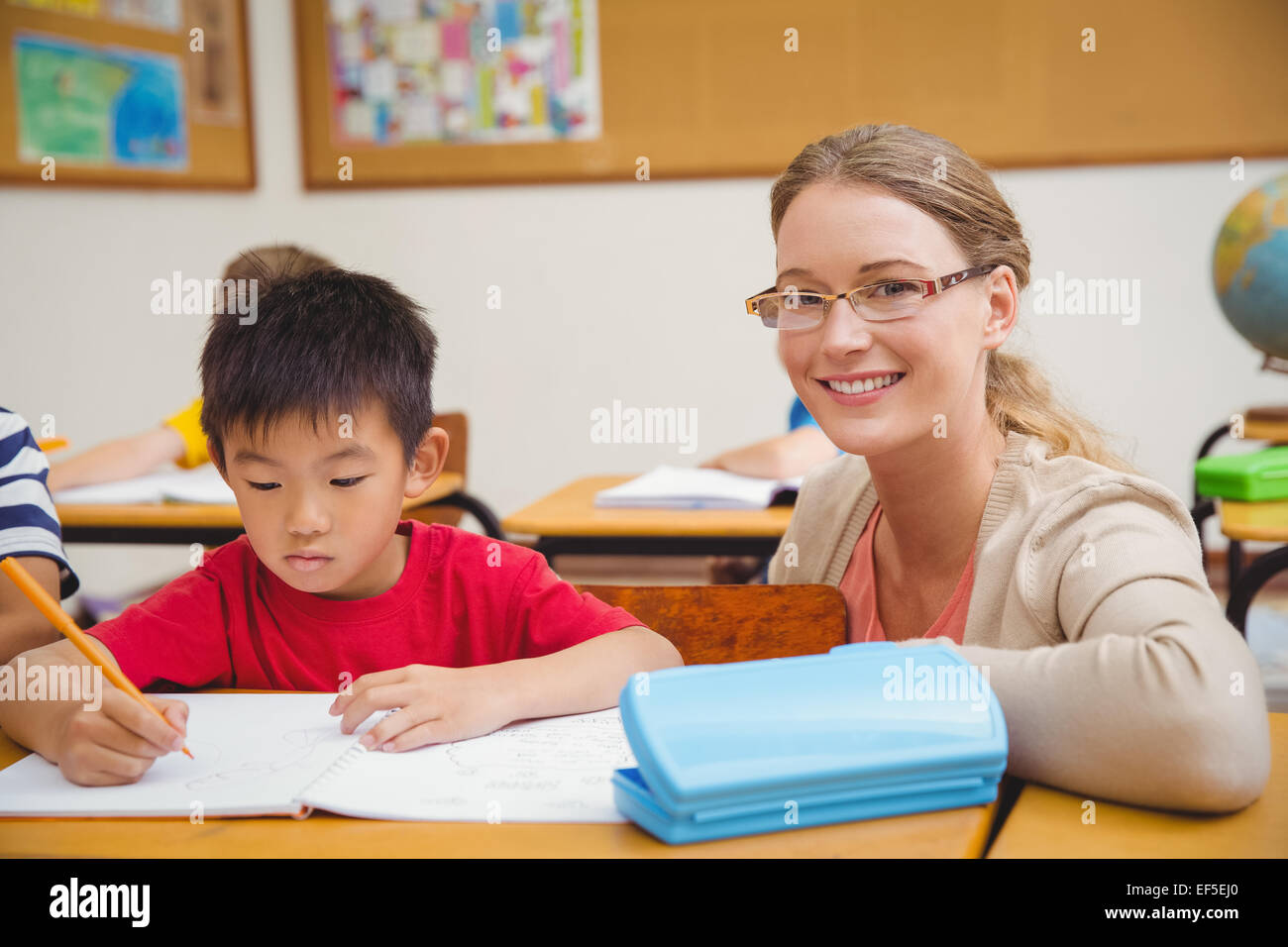 Pretty teacher helping pupil in classroom Stock Photo - Alamy