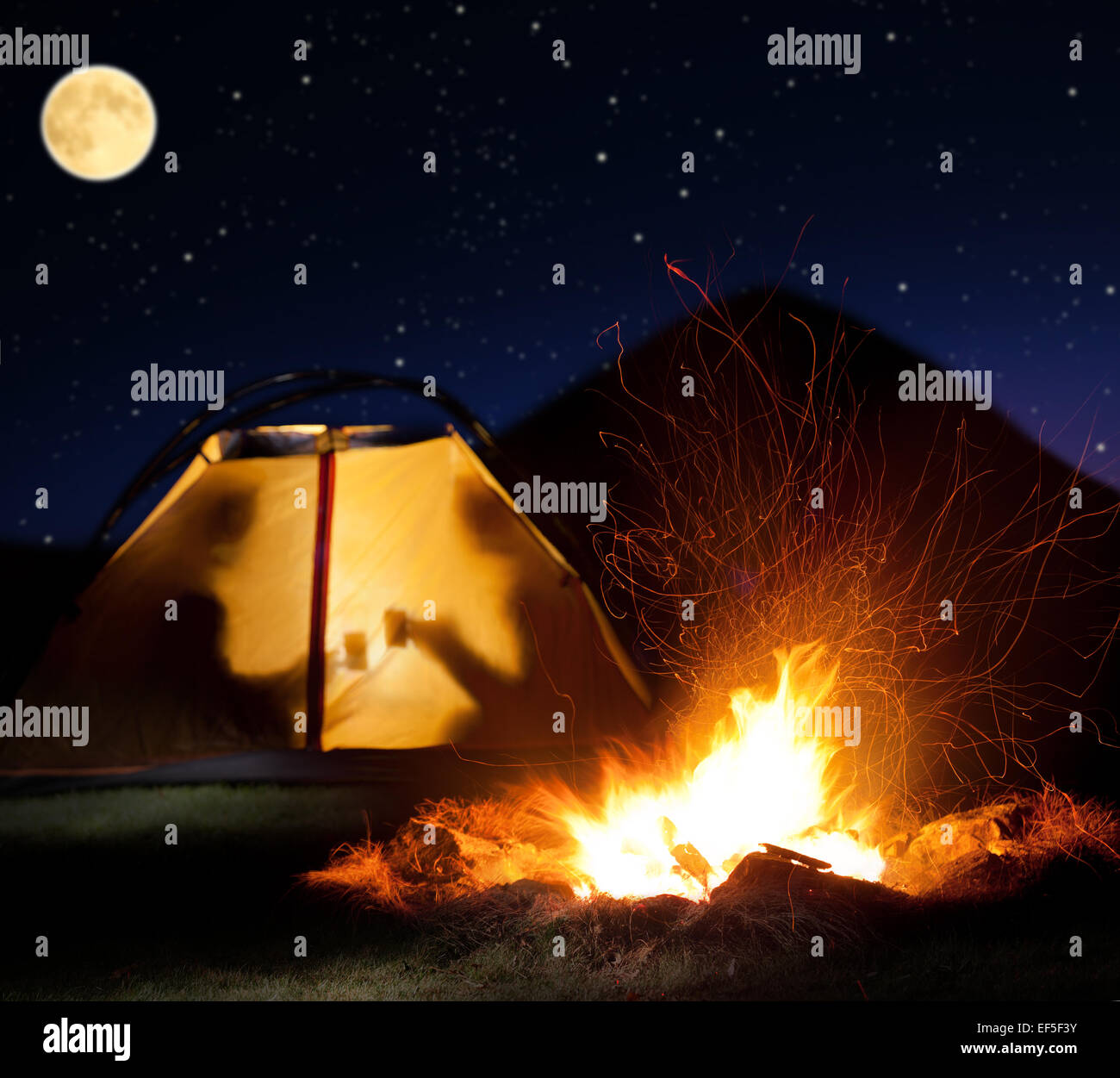 Camp shines at night. The campfire in the front as the symbol of ...