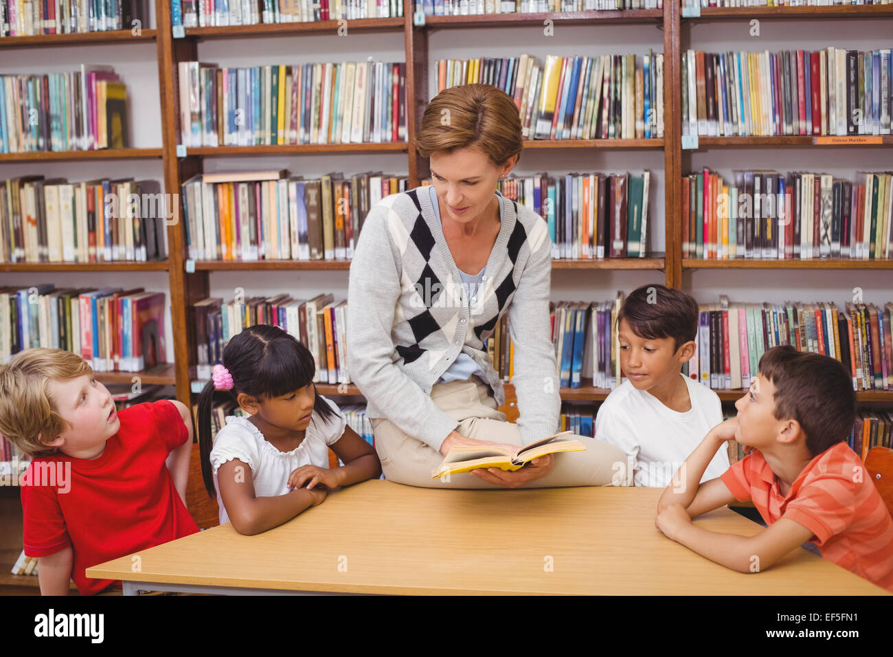 Cute pupils and teacher reading in library Stock Photo - Alamy
