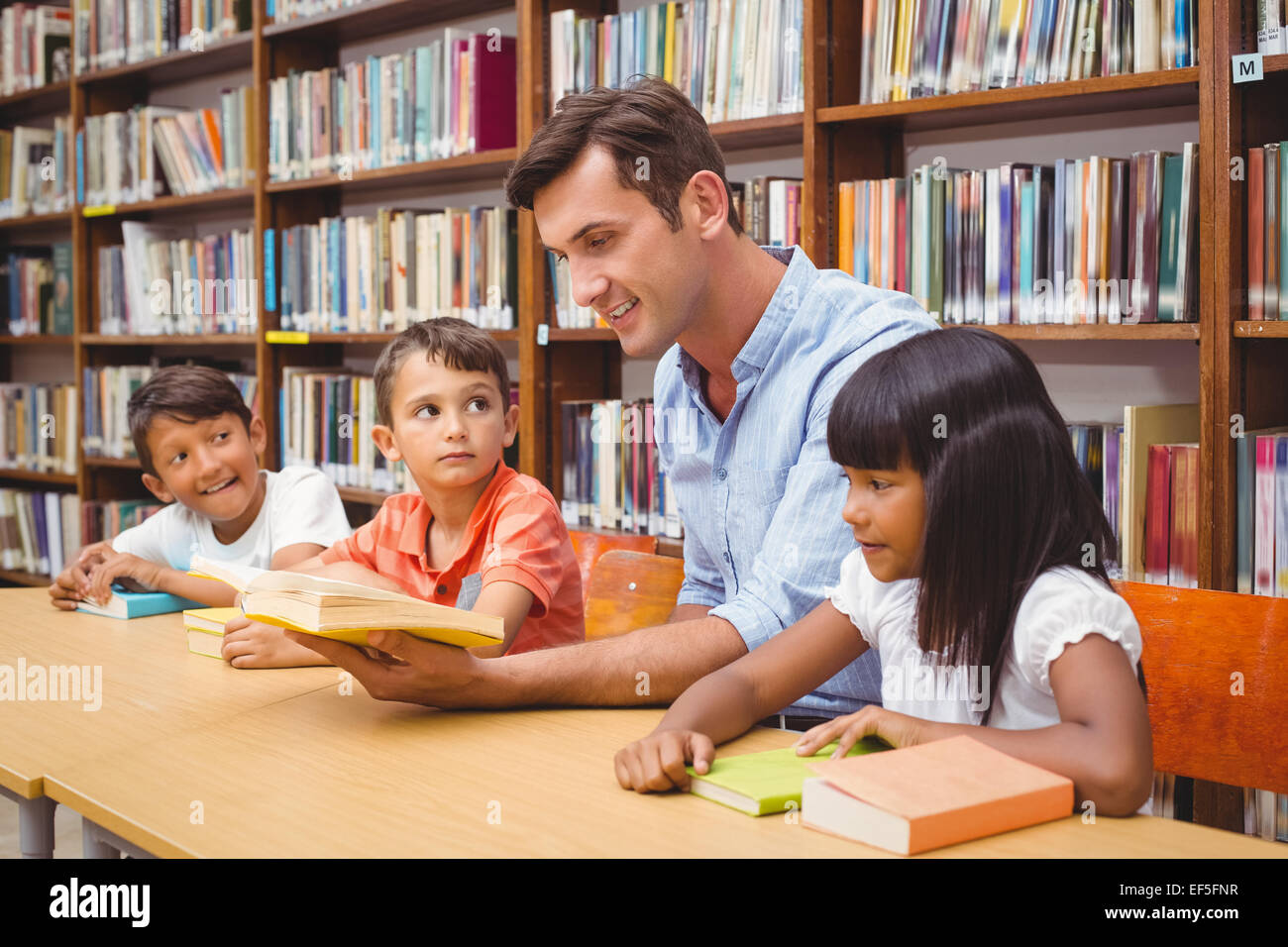Cute pupils and teacher reading in library Stock Photo - Alamy