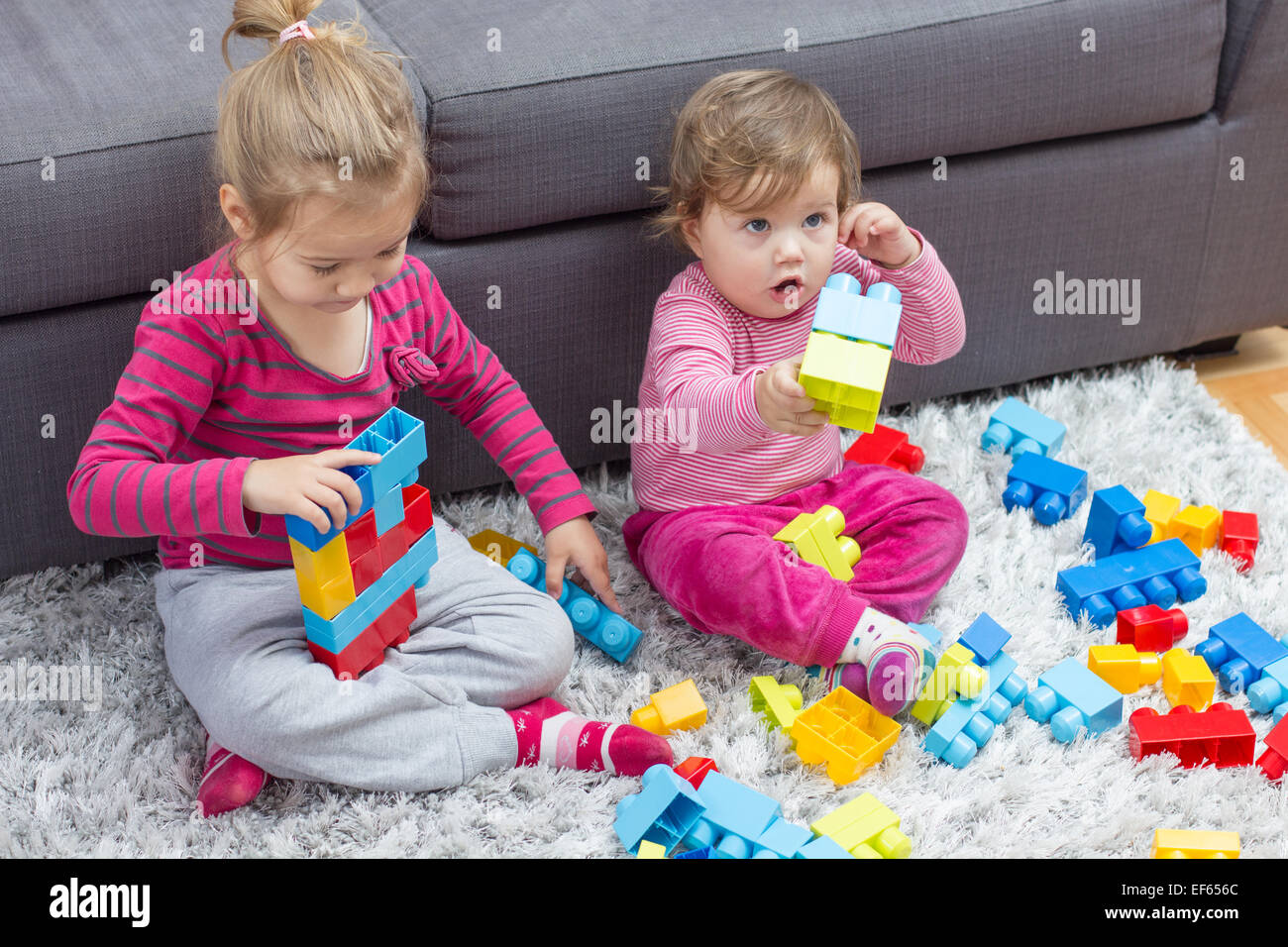 Little girl and baby playing together with colorful blocks at home ...
