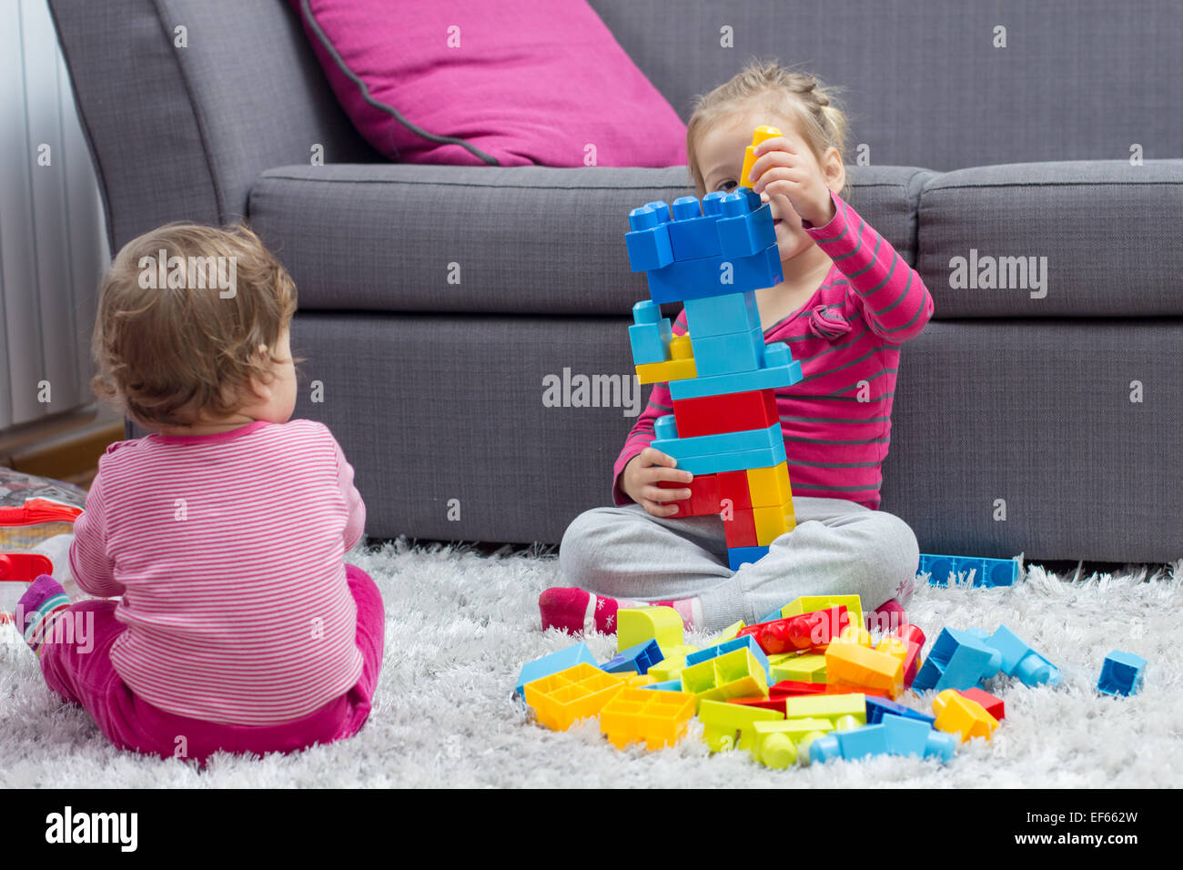 Little girl and baby playing together with colorful blocks at home ...