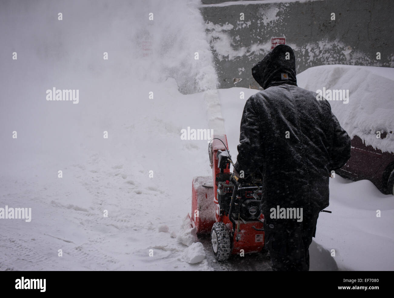 A man uses a snowblower to clear snow in a parking lot during a snow ...