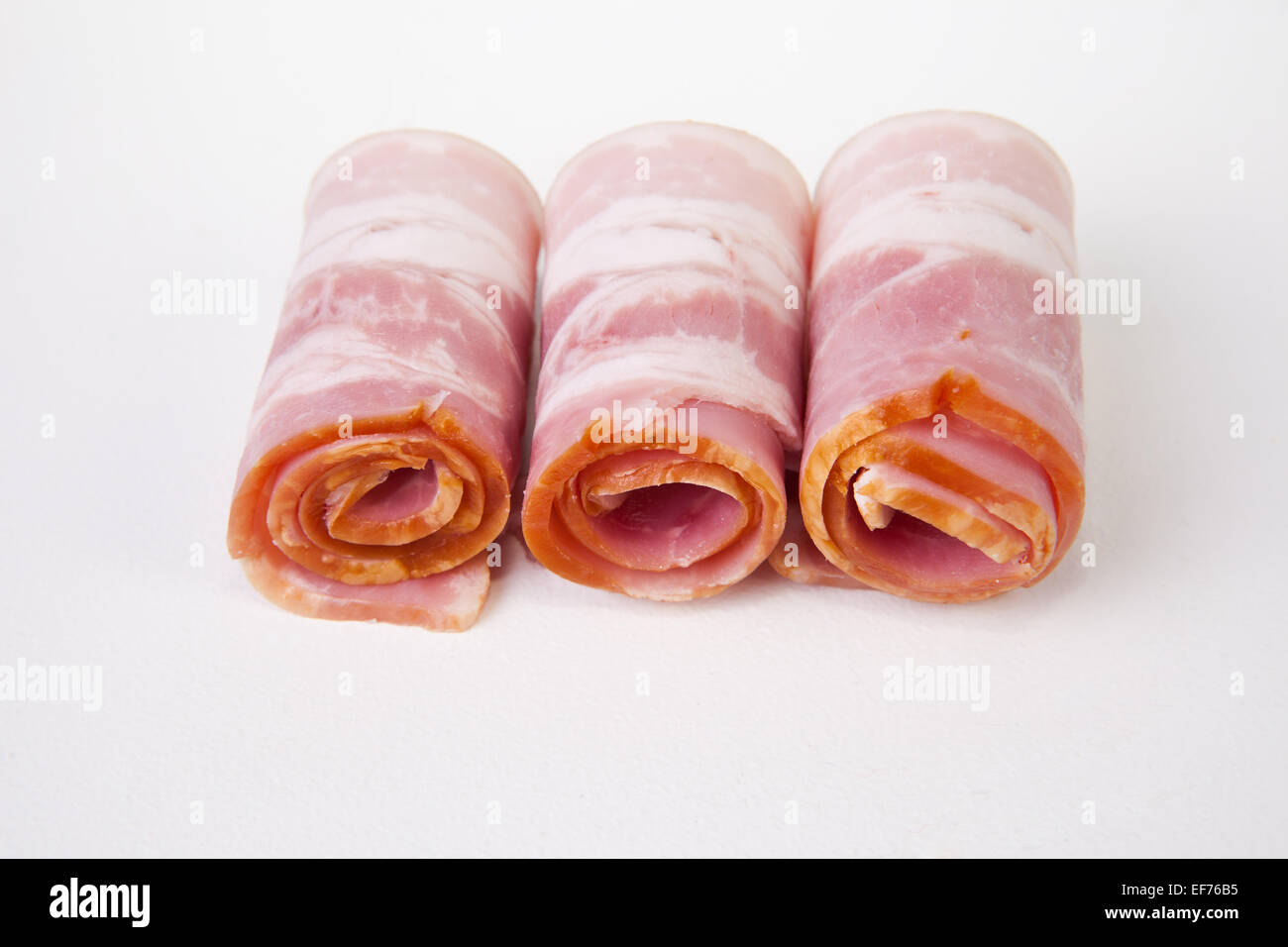 Three rolled raw bacon slices isolated on white background Stock Photo ...