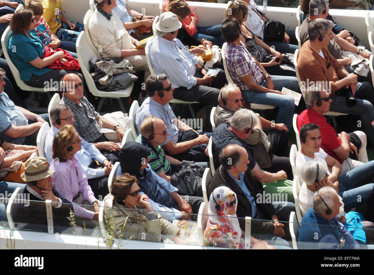 Tourists seated in a riverboat listening to tour guide on headphones ...
