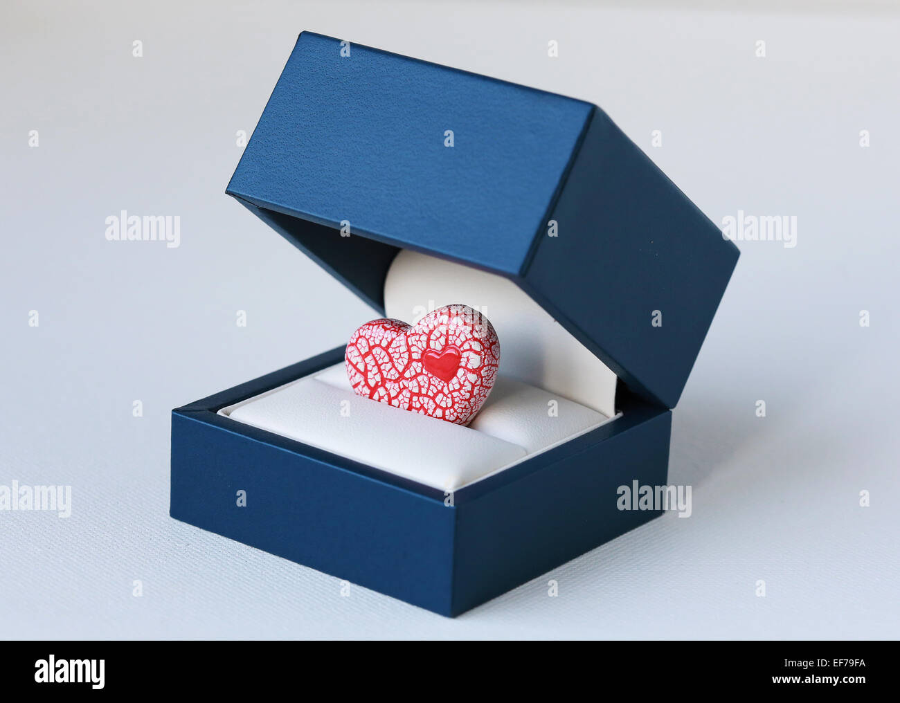 An image of a bright red and white ceramic heart inside a blue jewelry ...