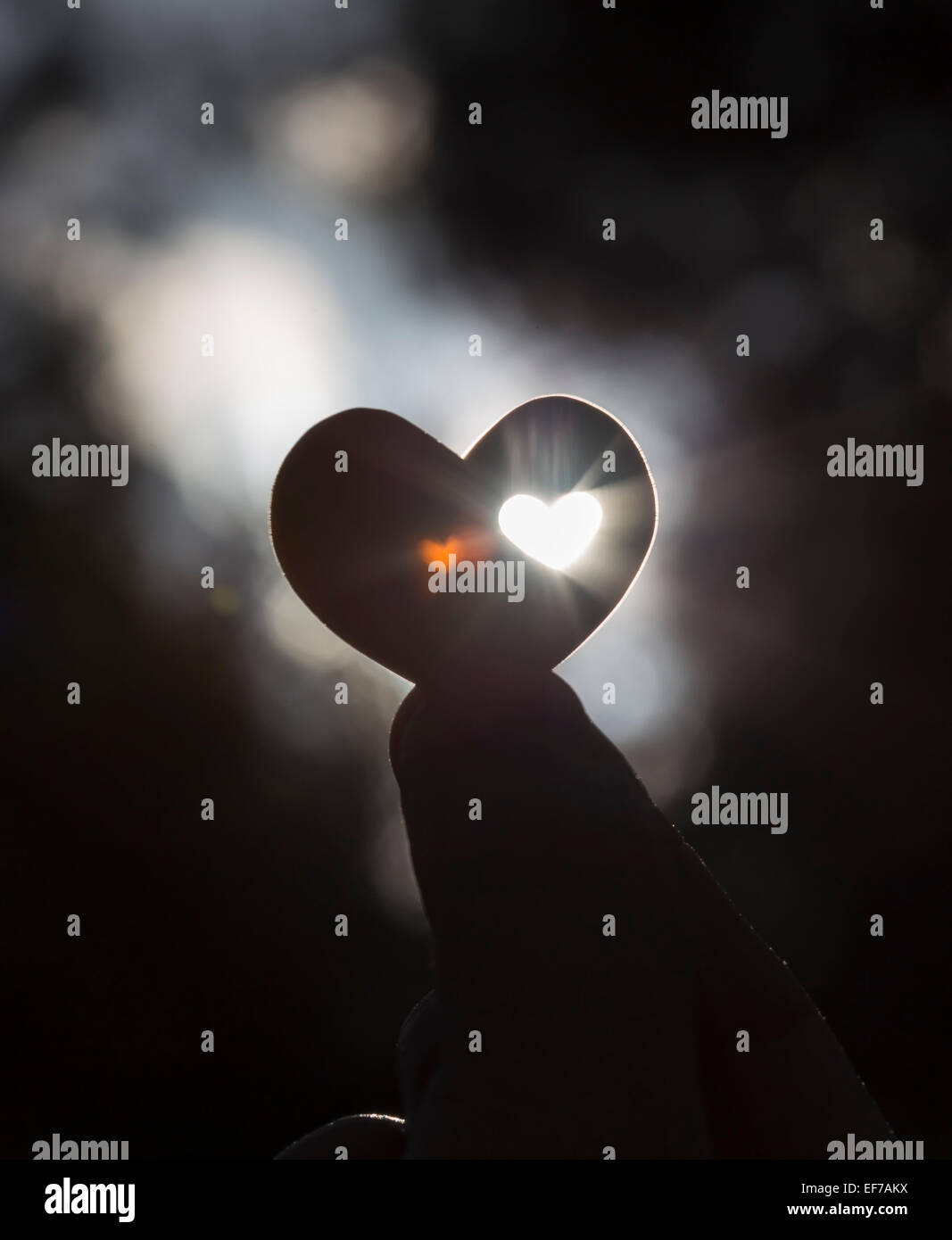 A hand holds a heart shape with a small heart shape inside it against ...