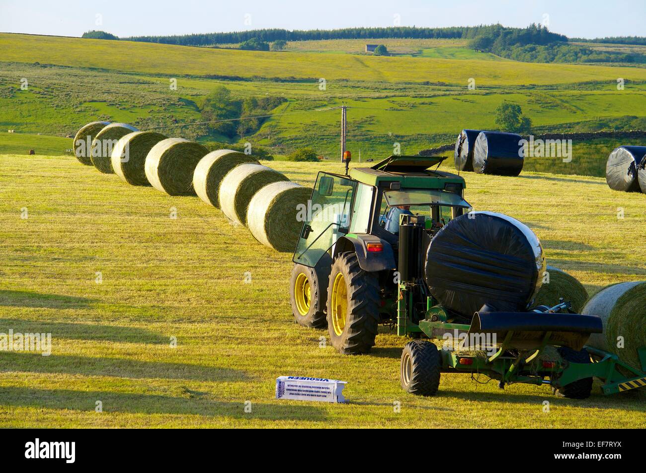 Silage bale being rapped in black plastic by a tractor in a field ...