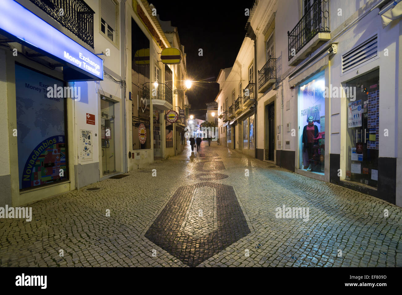Lagos cobbled street at night with a Bureau de Change sign illuminated ...
