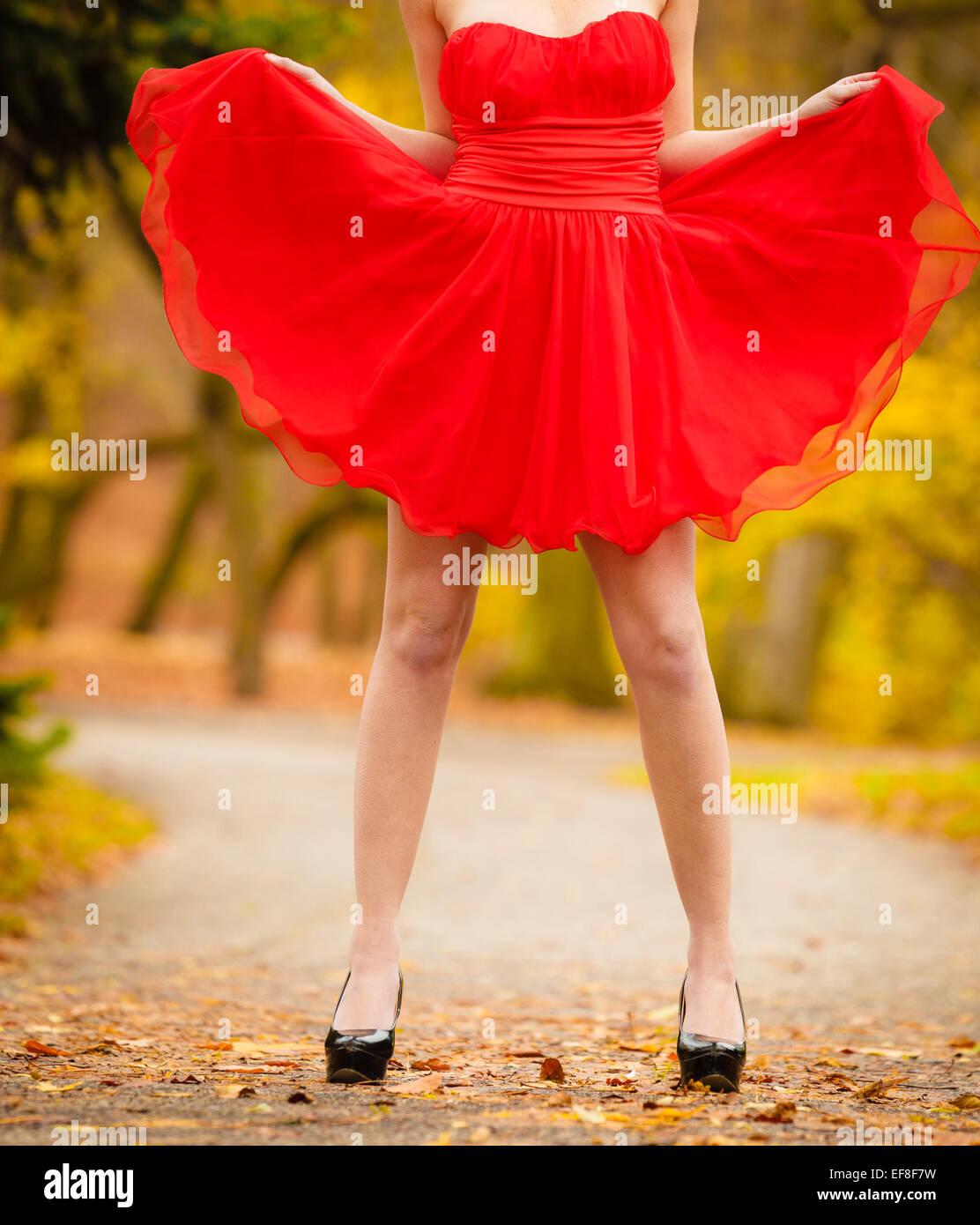 Full length fashionable elegant young woman in red dress outdoor relaxing walking in autumn park ...