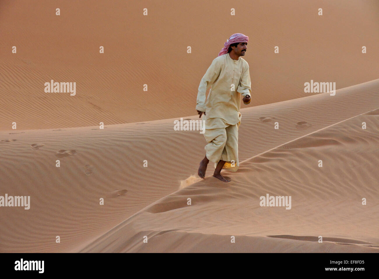 Arab man in traditional dress walking on sand dune of Liwa, Abu Dhabi ...