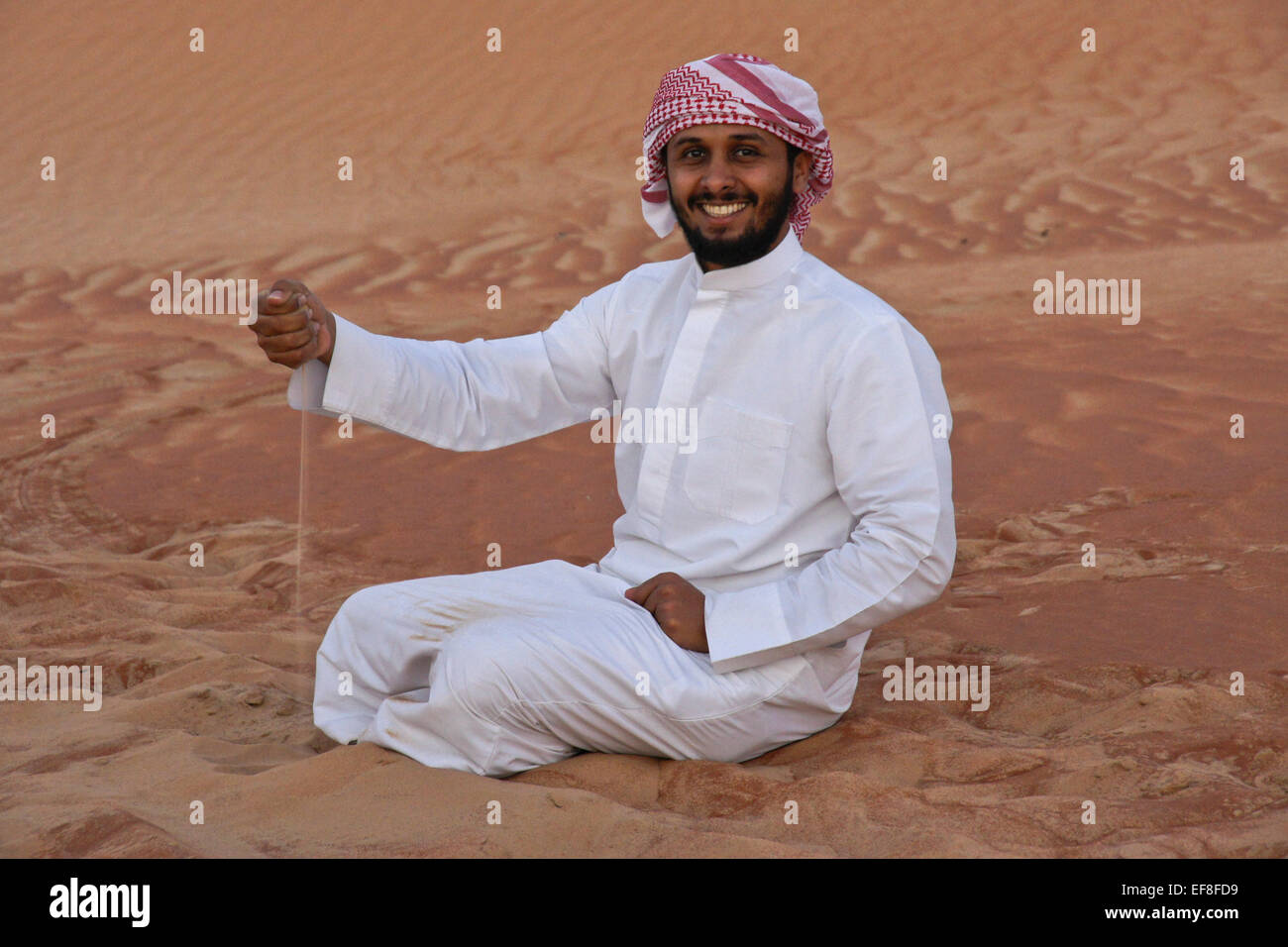 Arab man in traditional dress sitting in sand dunes of Liwa, Abu Dhabi ...