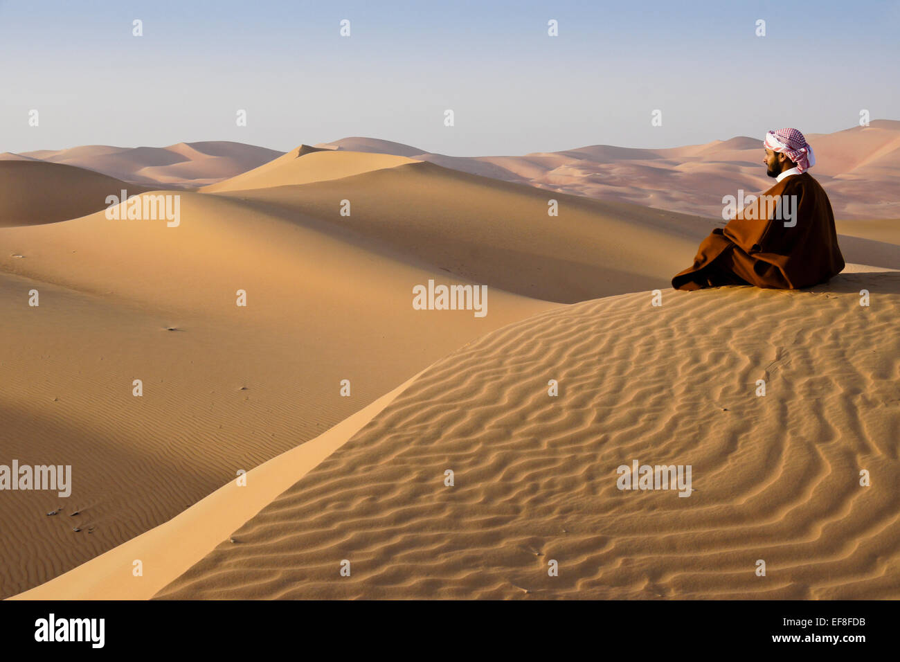 Man in traditional dress sitting in sand dunes of Liwa, Abu Dhabi, UAE ...