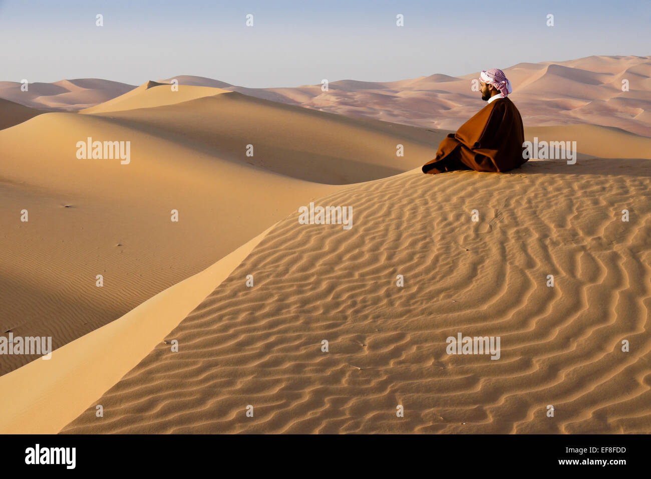 Man in traditional dress sitting in sand dunes of Liwa, Abu Dhabi, UAE ...